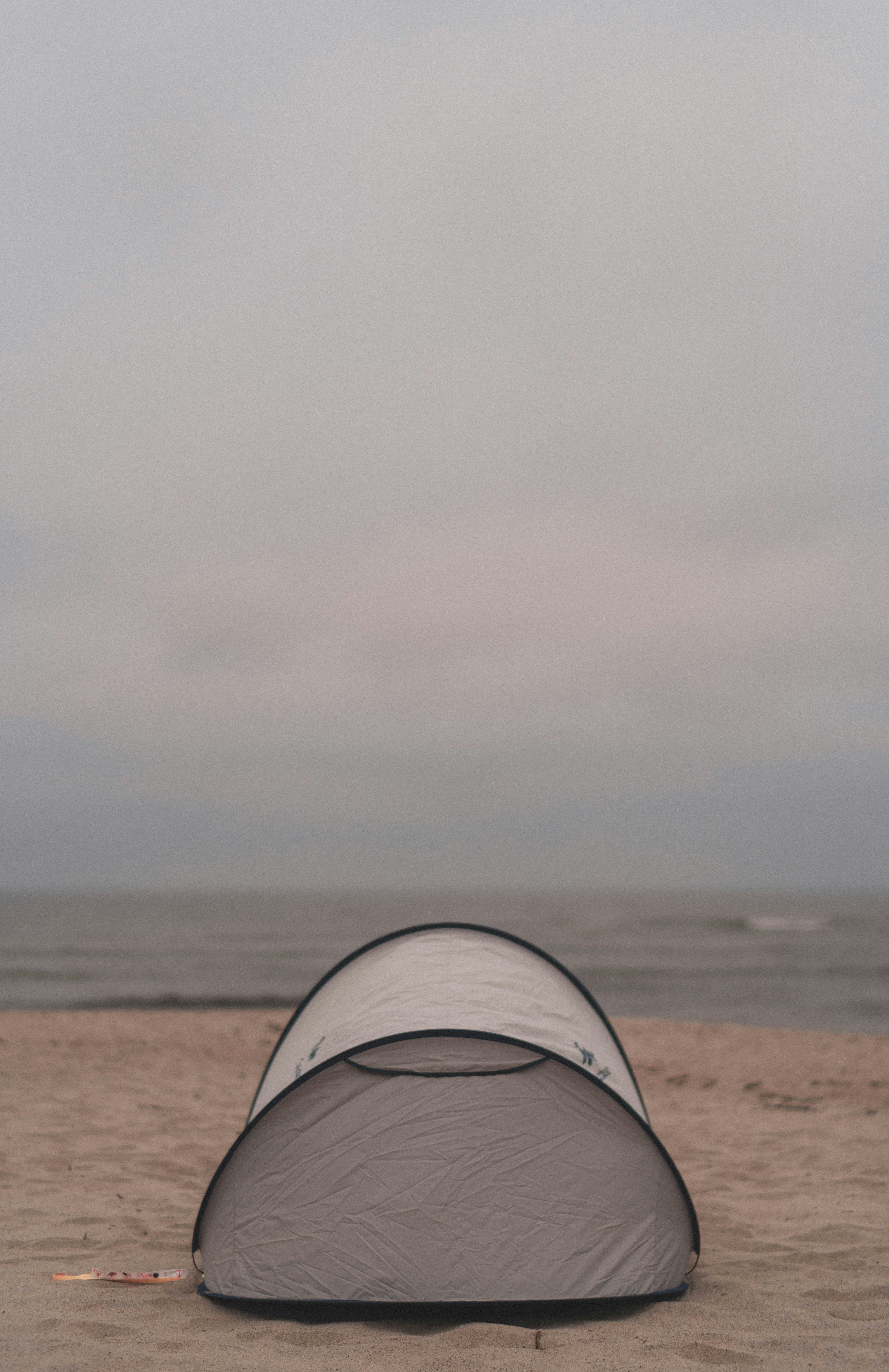 A gray pop-up tent sits on a sandy beach, framed by a moody sky and gentle ocean waves in the background.