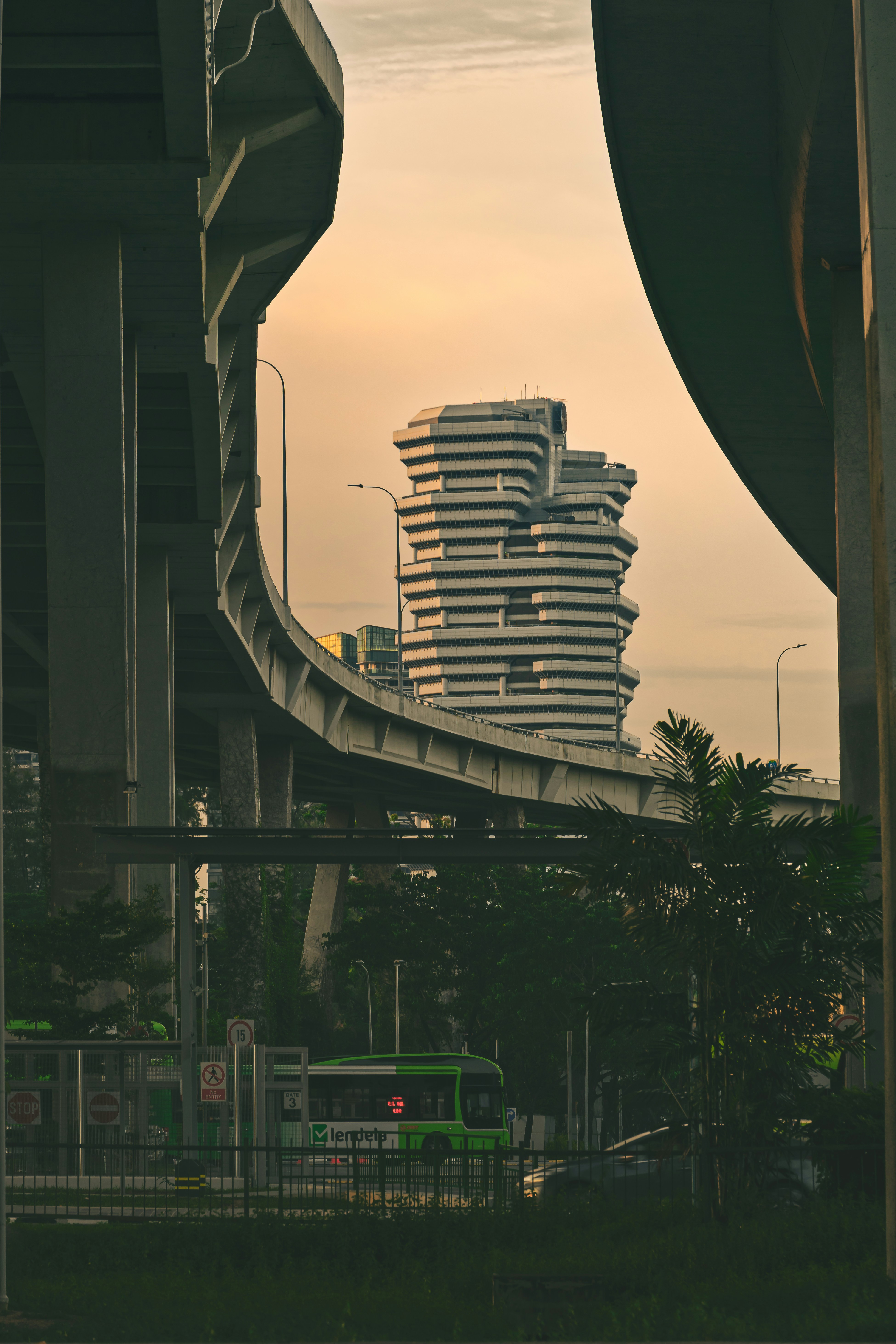 Modern architectural structure framed by overpasses, showcasing the interplay of urban design and nature. A bus is partially visible in the foreground.