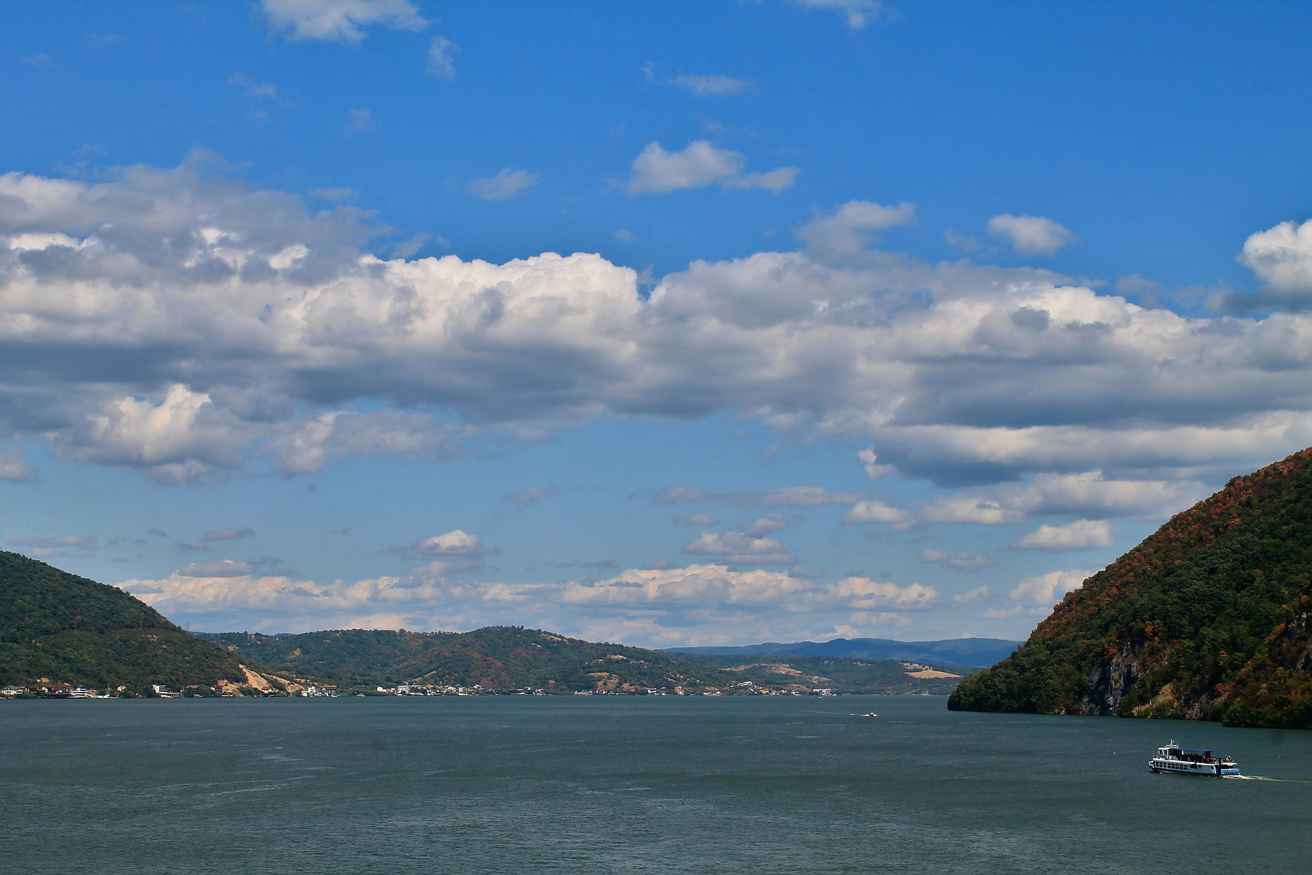 Image taken above the Small Cauldron of the Danube. It is situated between the Romanian and Serbian boarder (Serbia on the right and Romania on the left). | a boat floating on top of a large body of water