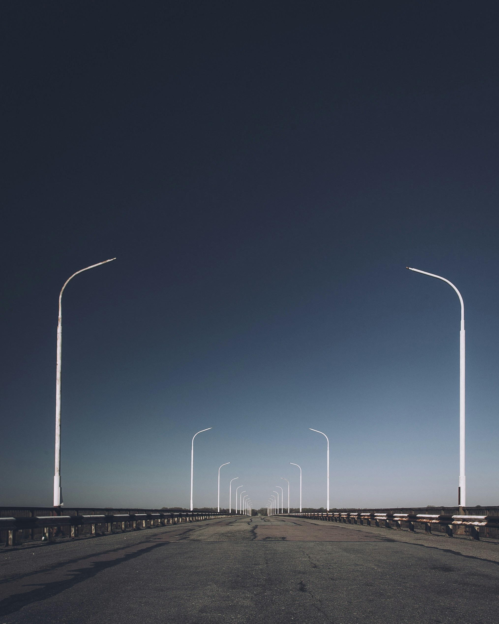 A deserted road stretches into the horizon, framed by tall streetlights against a gradient sky. The scene evokes a sense of isolation and tranquility.