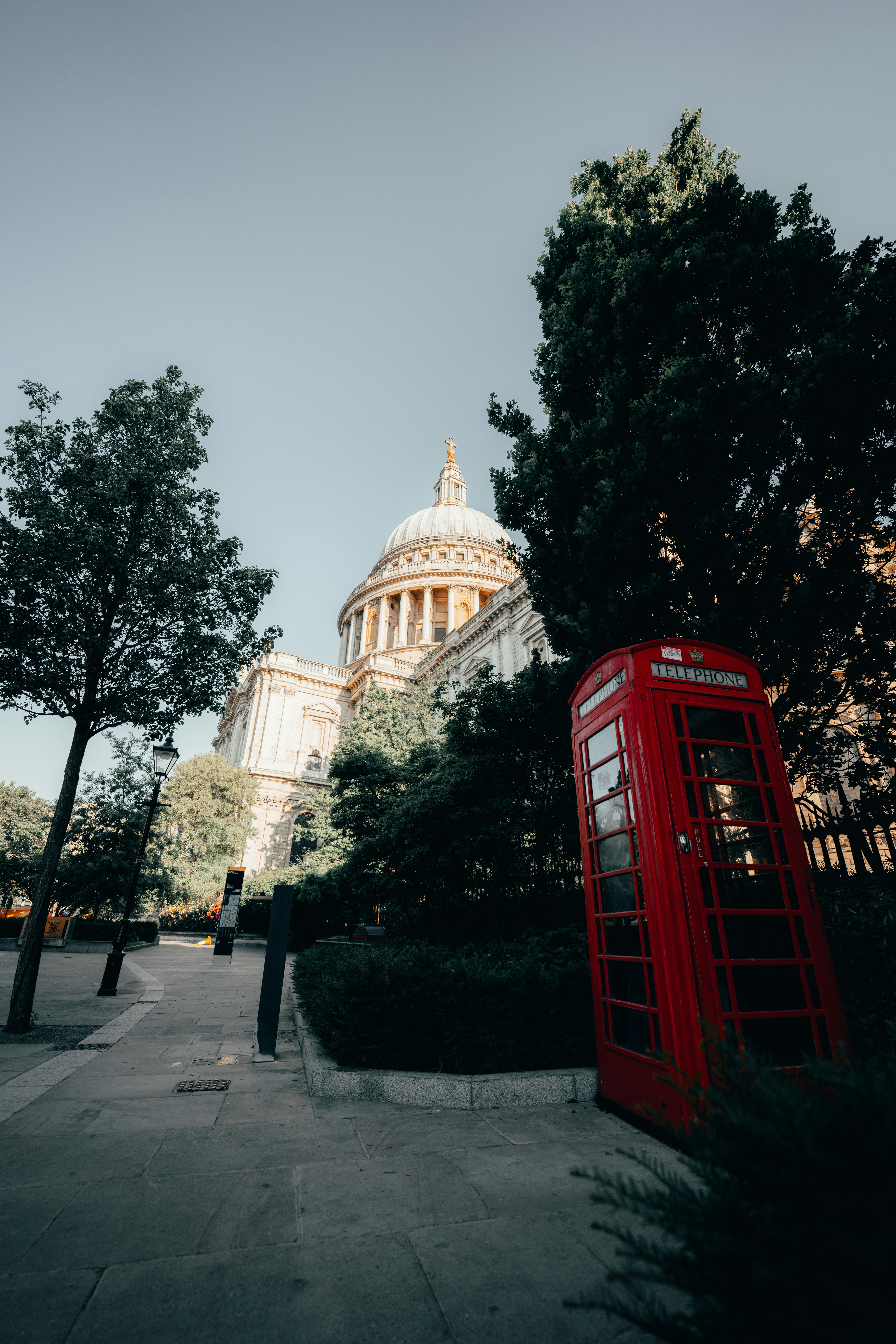 A classic red telephone booth stands prominently in a lush green park, framed by the grand architecture of St. Paul's Cathedral in the background.