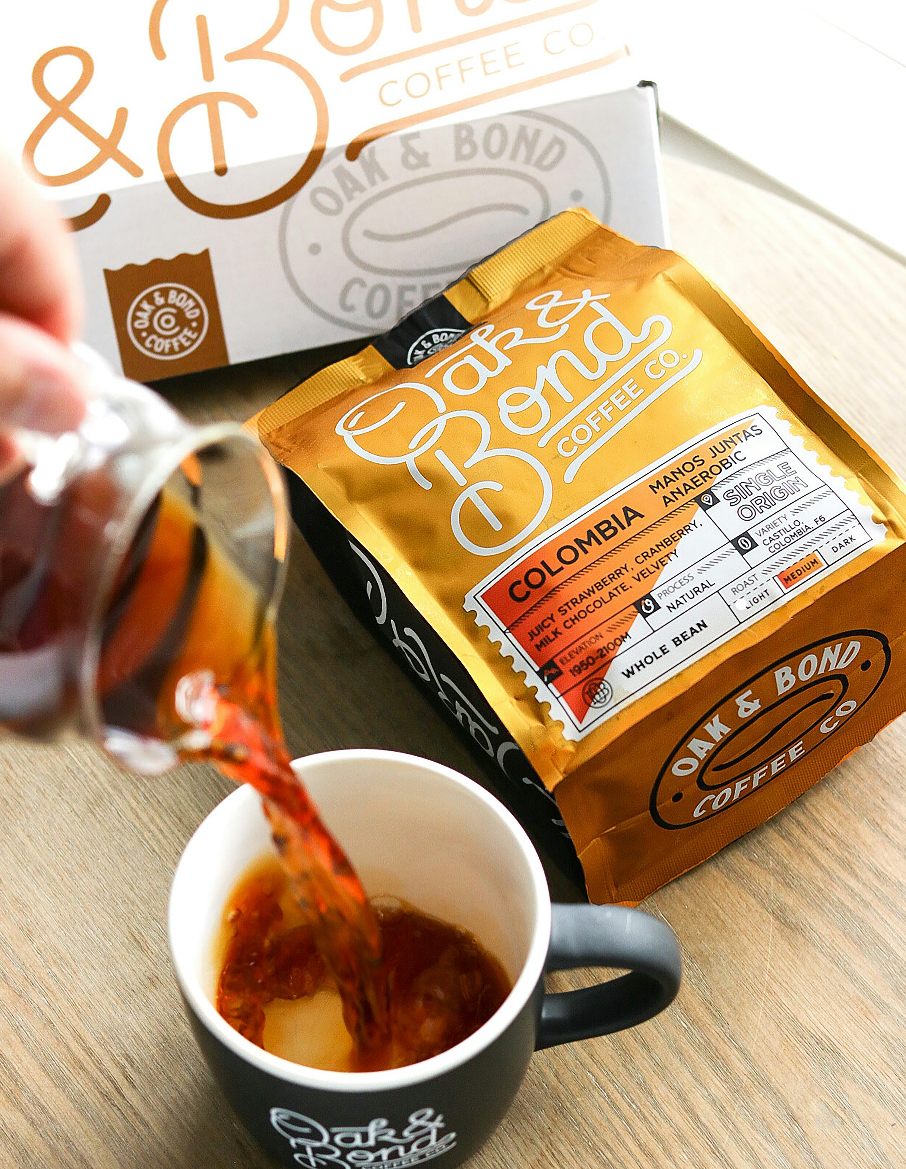 Pouring freshly brewed coffee from a glass carafe into a mug beside a vibrant coffee bag. The scene highlights the joy of coffee preparation.