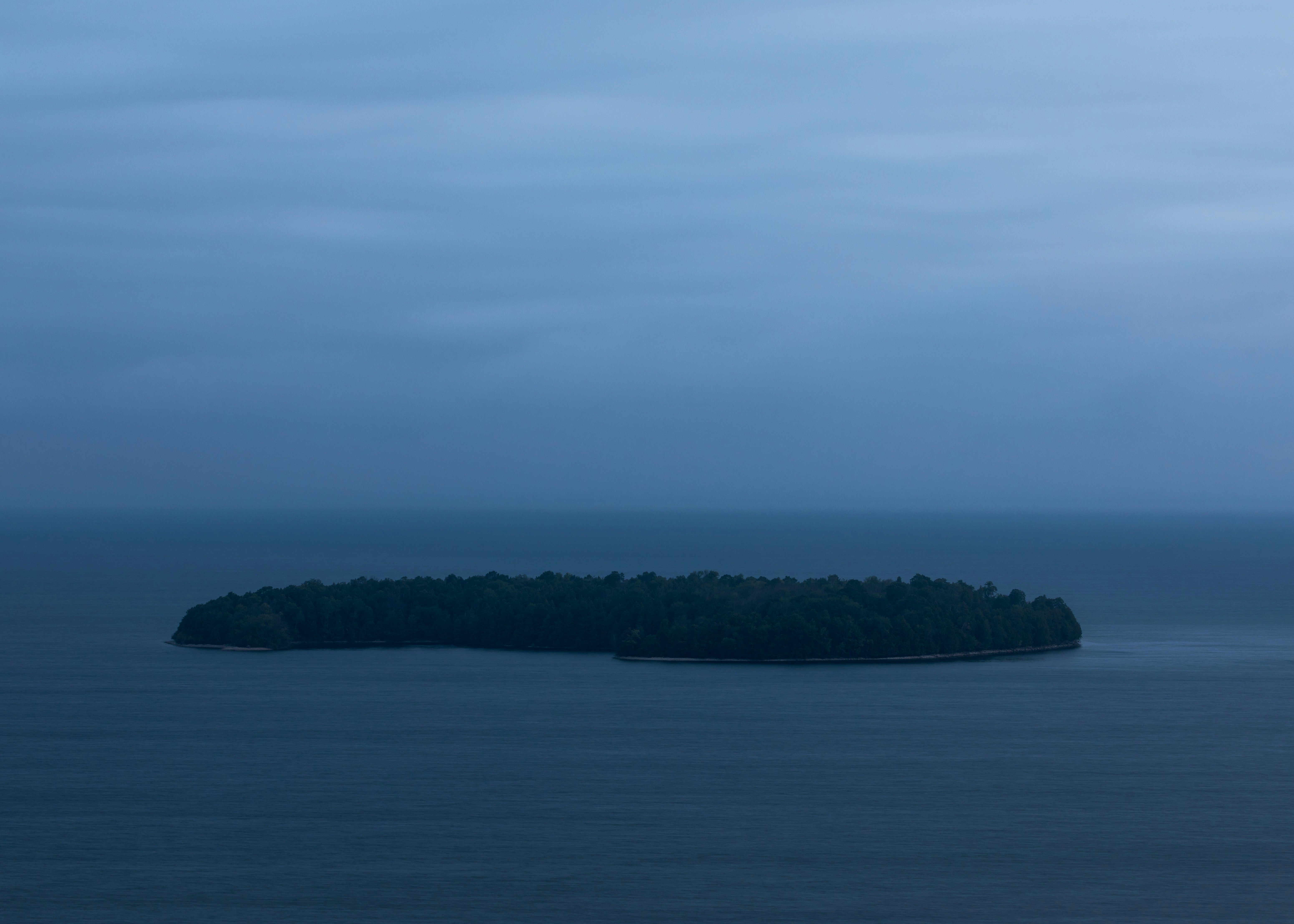 A secluded island emerges from the tranquil waters under a dusky sky, surrounded by gentle waves. The scene evokes a sense of calm and solitude.