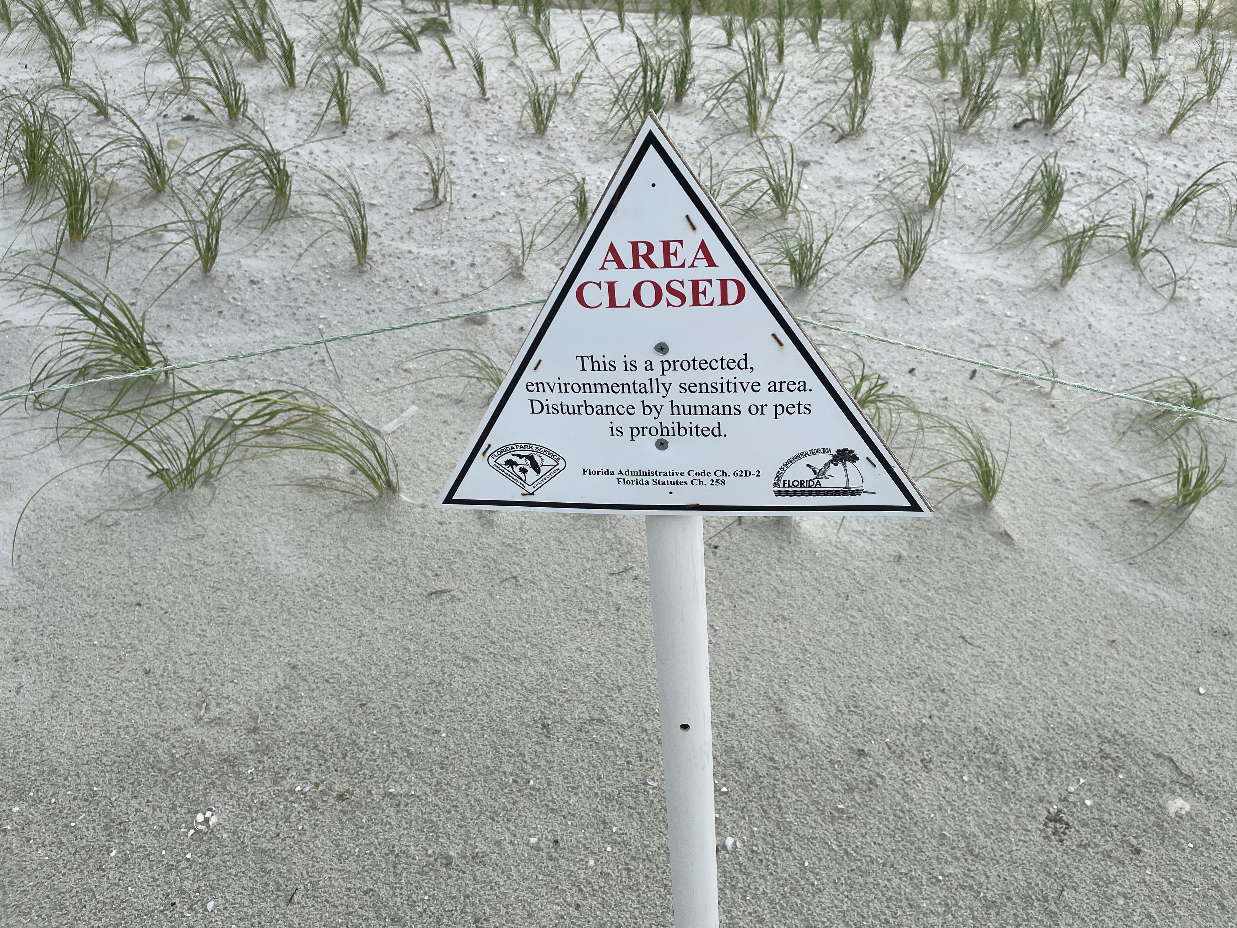 Triangular Warning: Area Closed Sign on a Sandy Dune