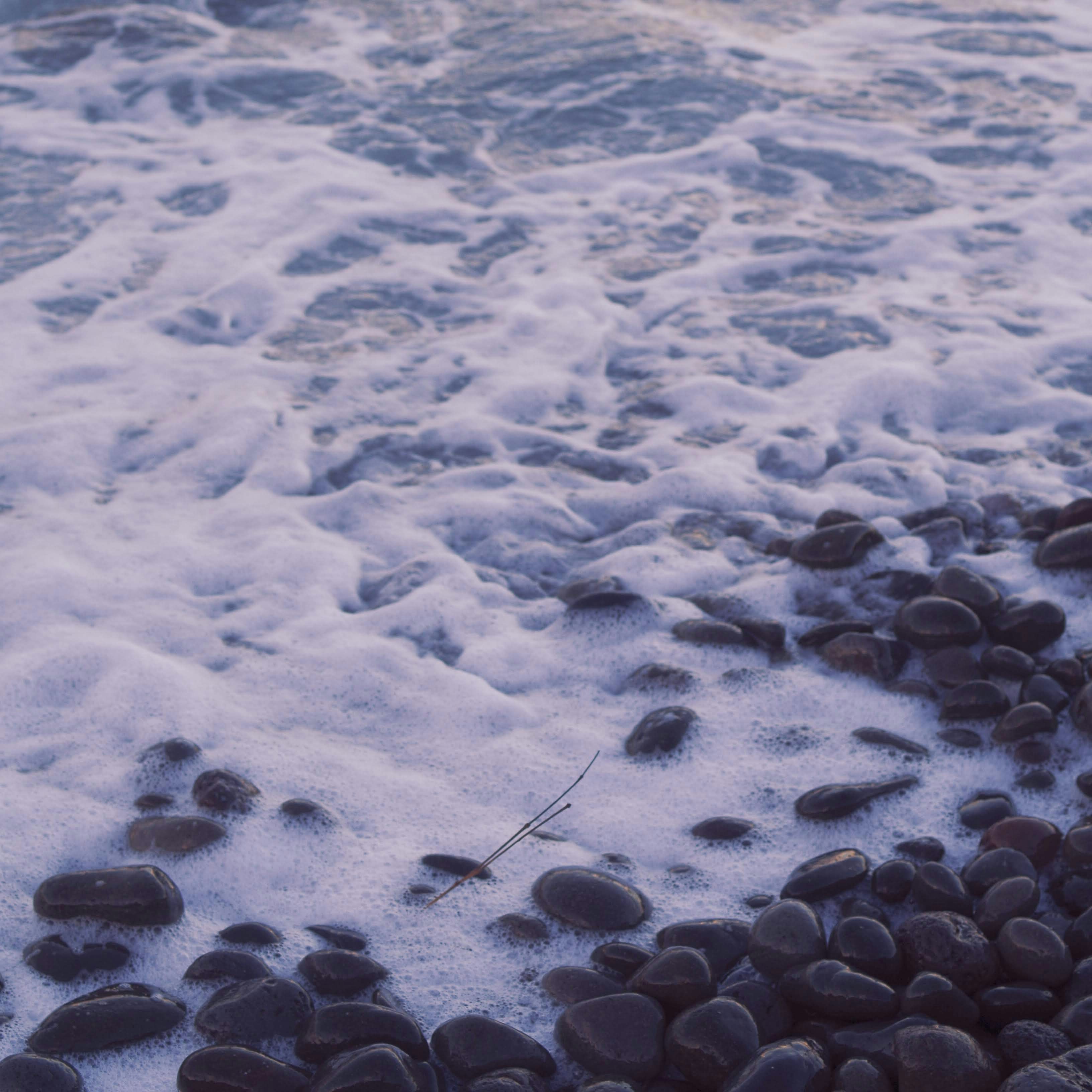 Gentle waves caress smooth pebbles along a tranquil shoreline, creating a serene coastal atmosphere.