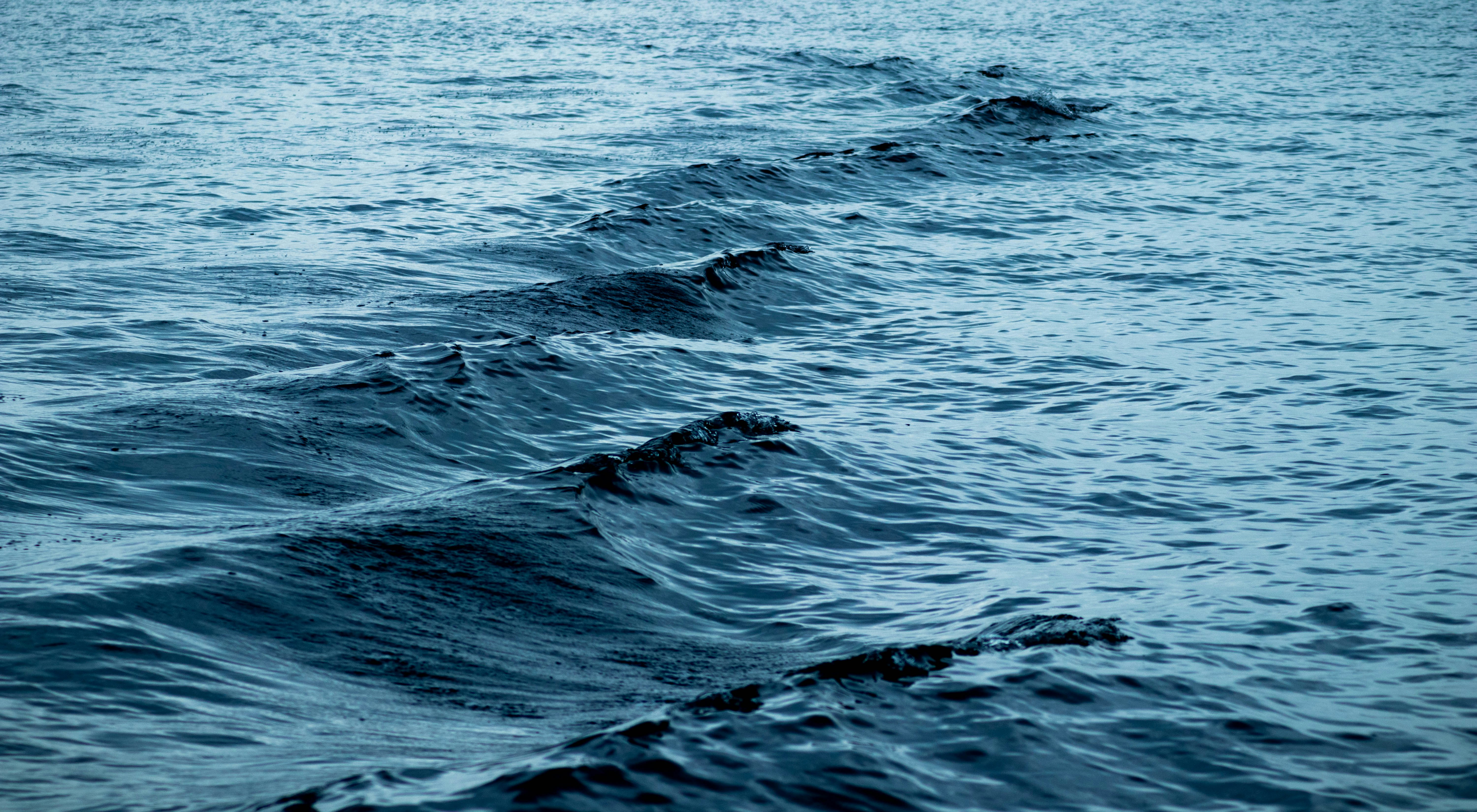 Vessel wake creating a series of rhythmic waves on a calm ocean surface.