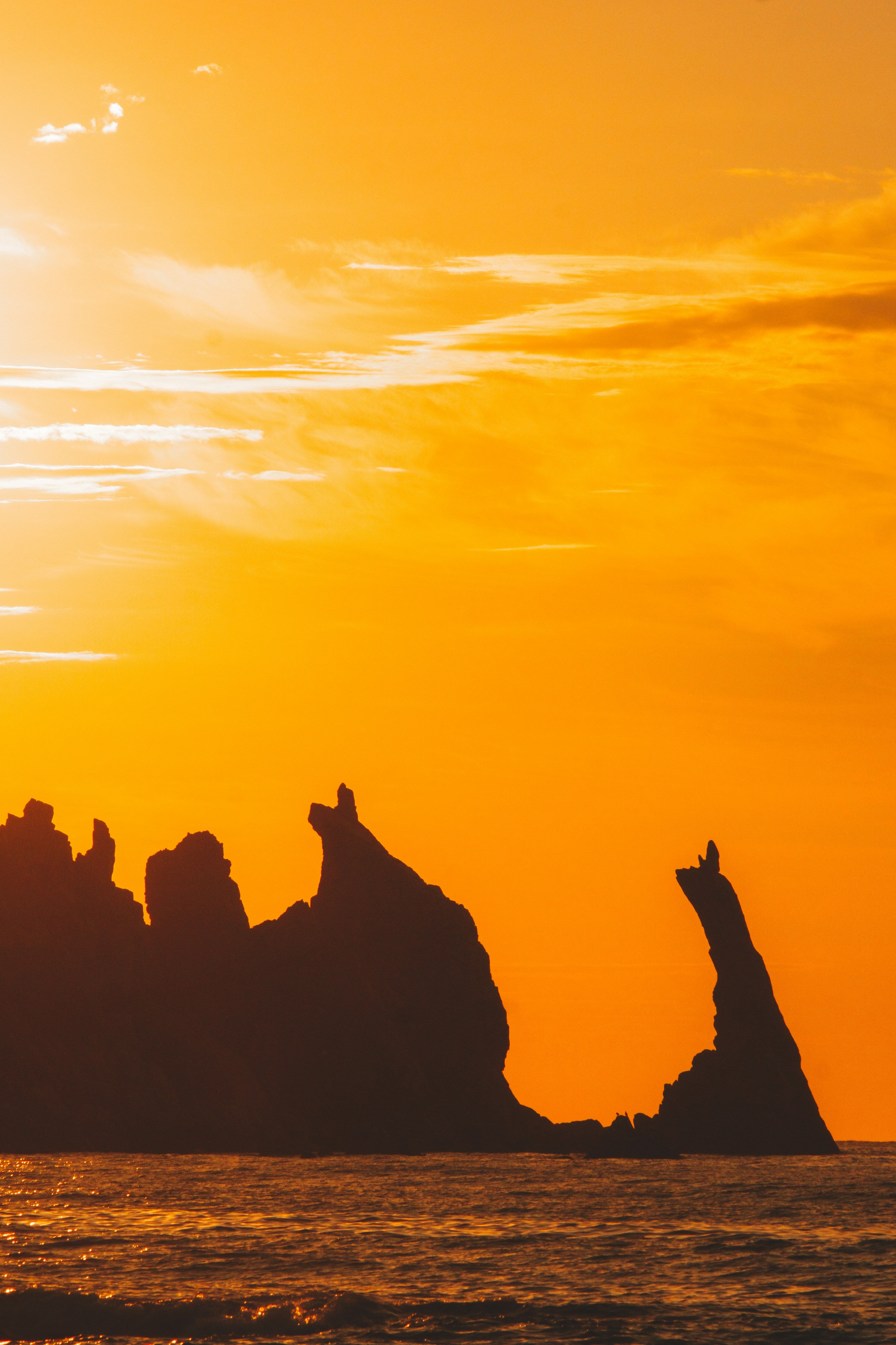 Dark rock formations silhouetted against a vibrant orange sunset, with soft clouds adding texture to the sky.
