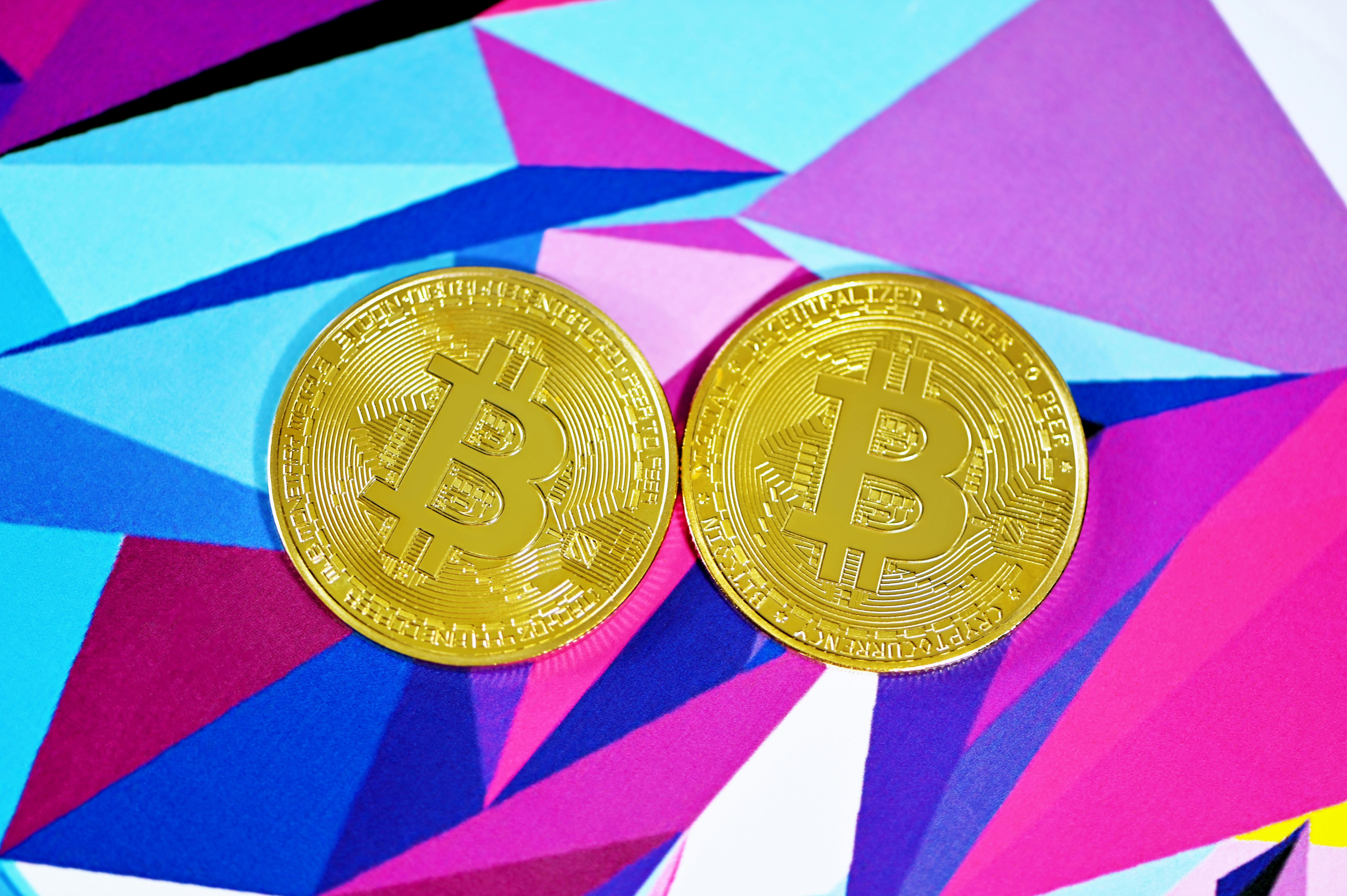 Two gold bitcoins sitting side by side on a colorful background photo ...