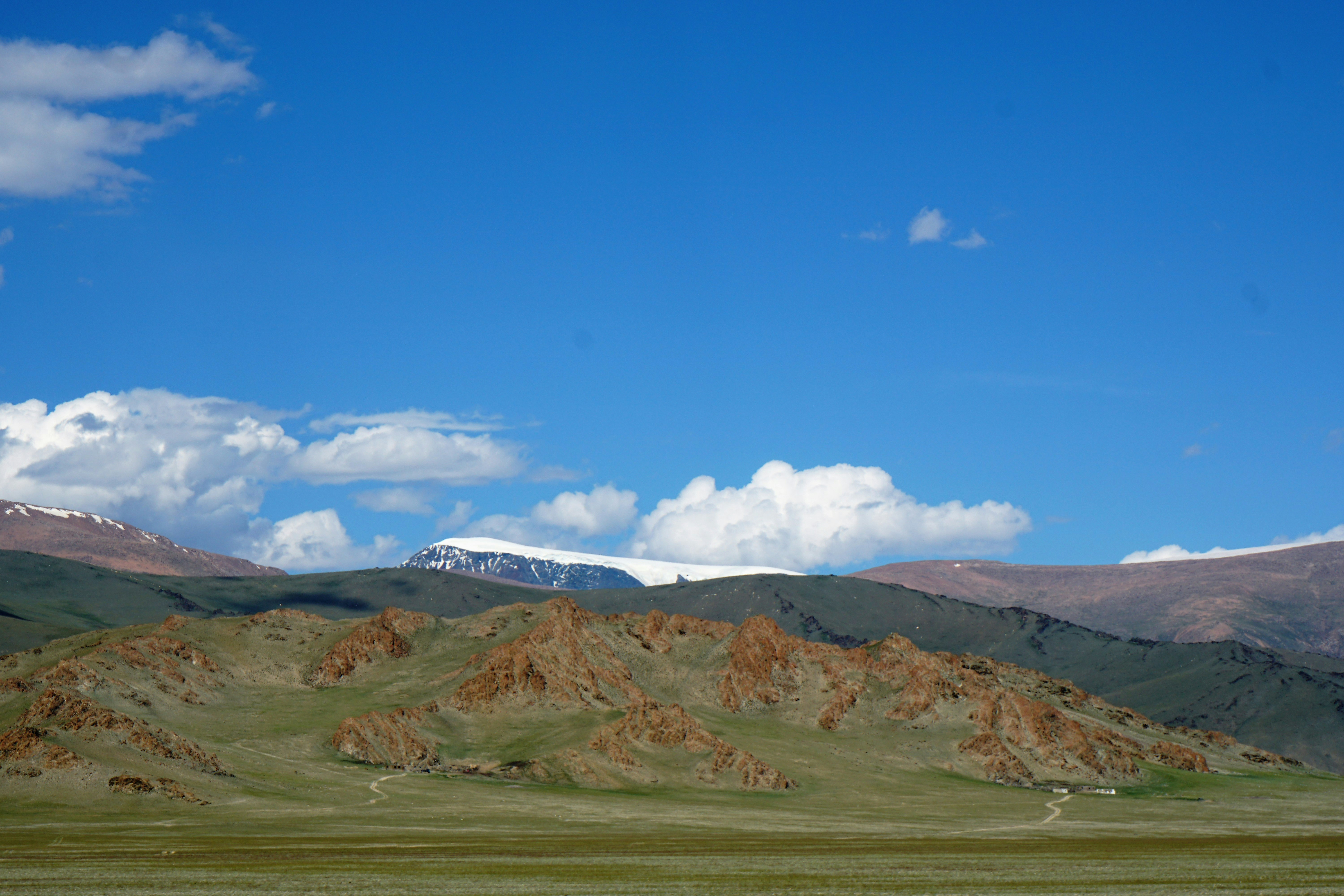 Vast green plains dotted with rugged red hills under a bright blue sky, showcasing the natural beauty of highland landscapes.
