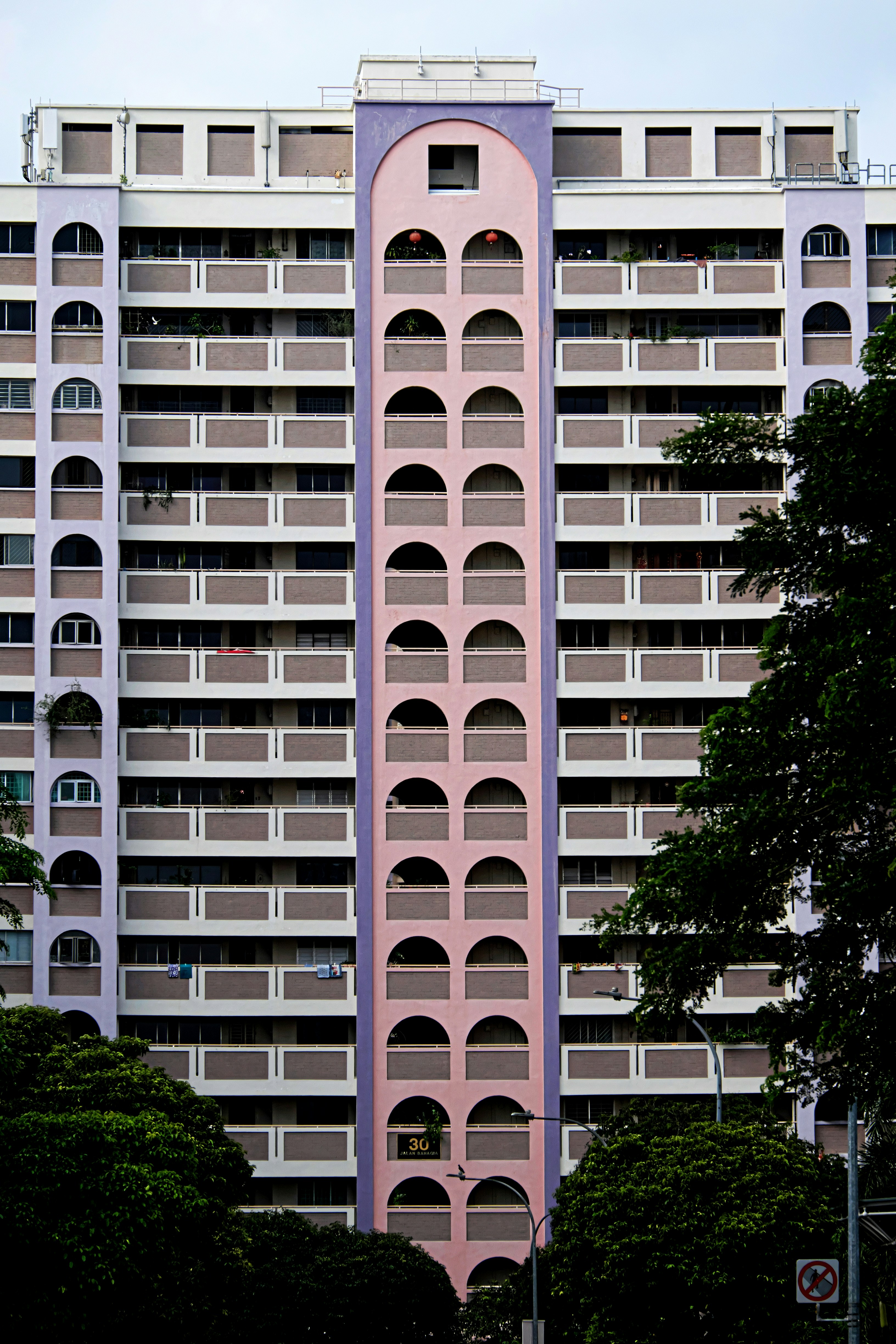 Colorful apartment building featuring a series of arches and balconies, surrounded by lush greenery.