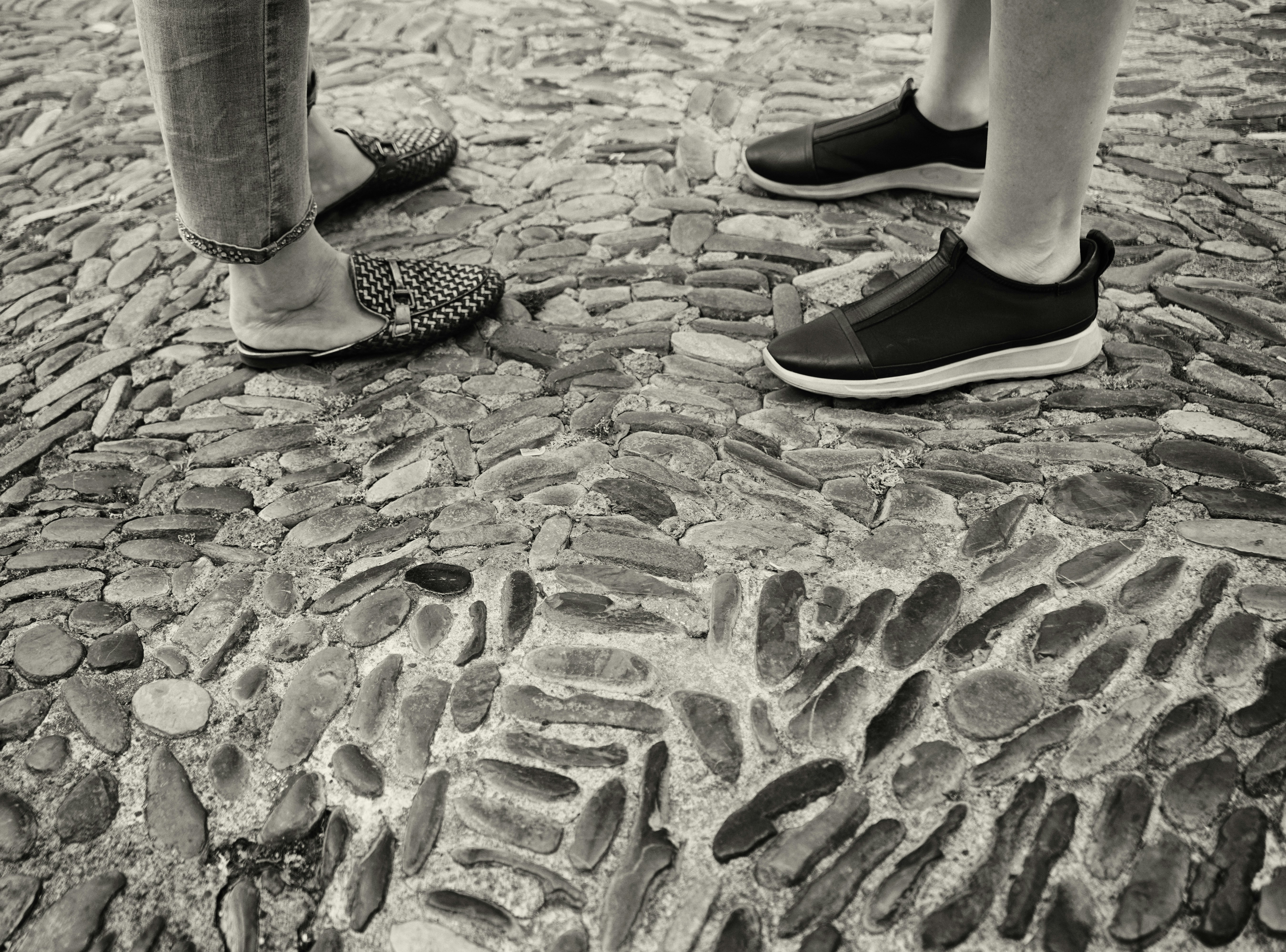 A couple of people standing on a cobblestone road photo – Free Human ...