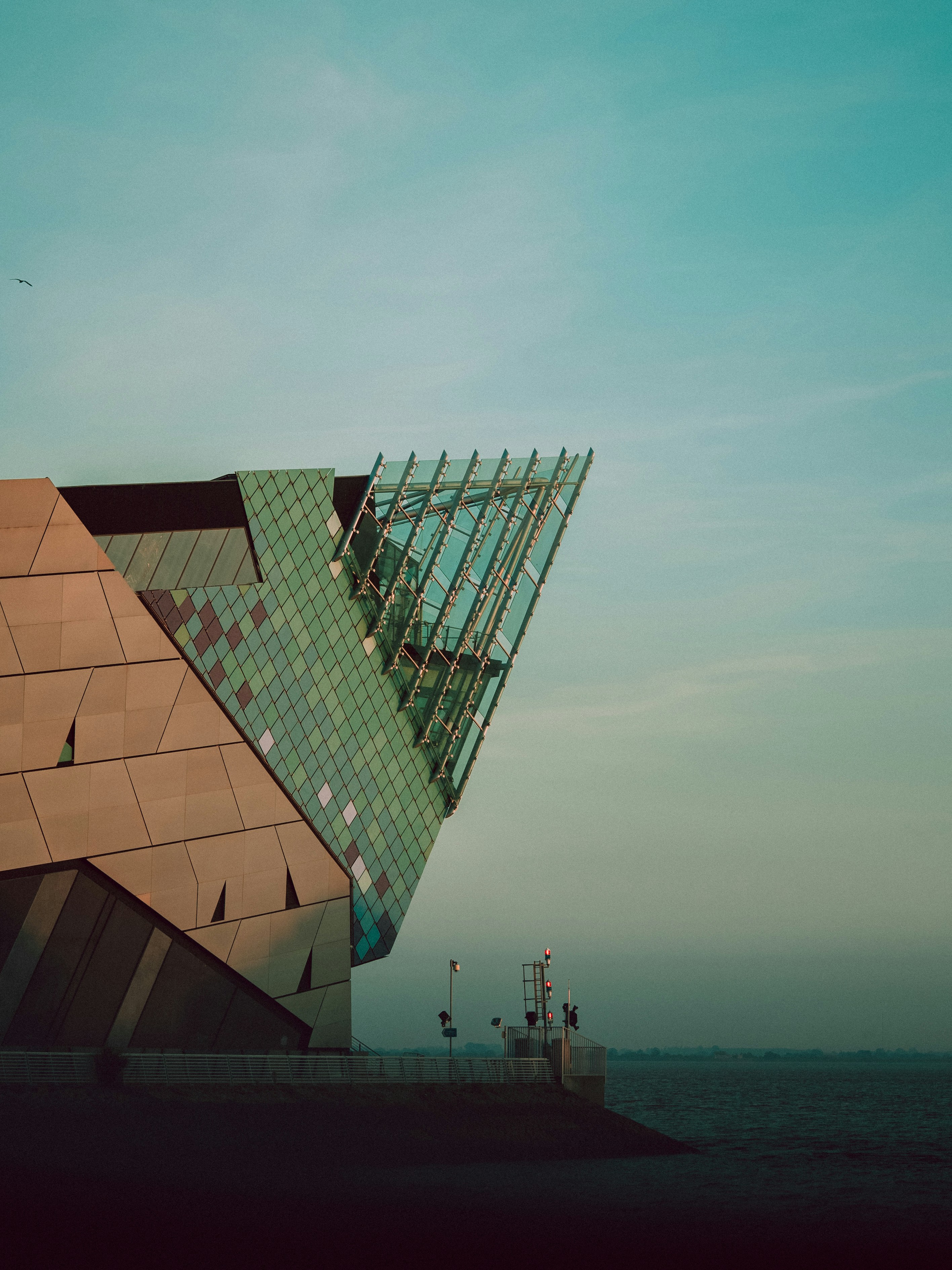 Modern building with angular design and glass elements reflecting soft evening light, situated by the water's edge.