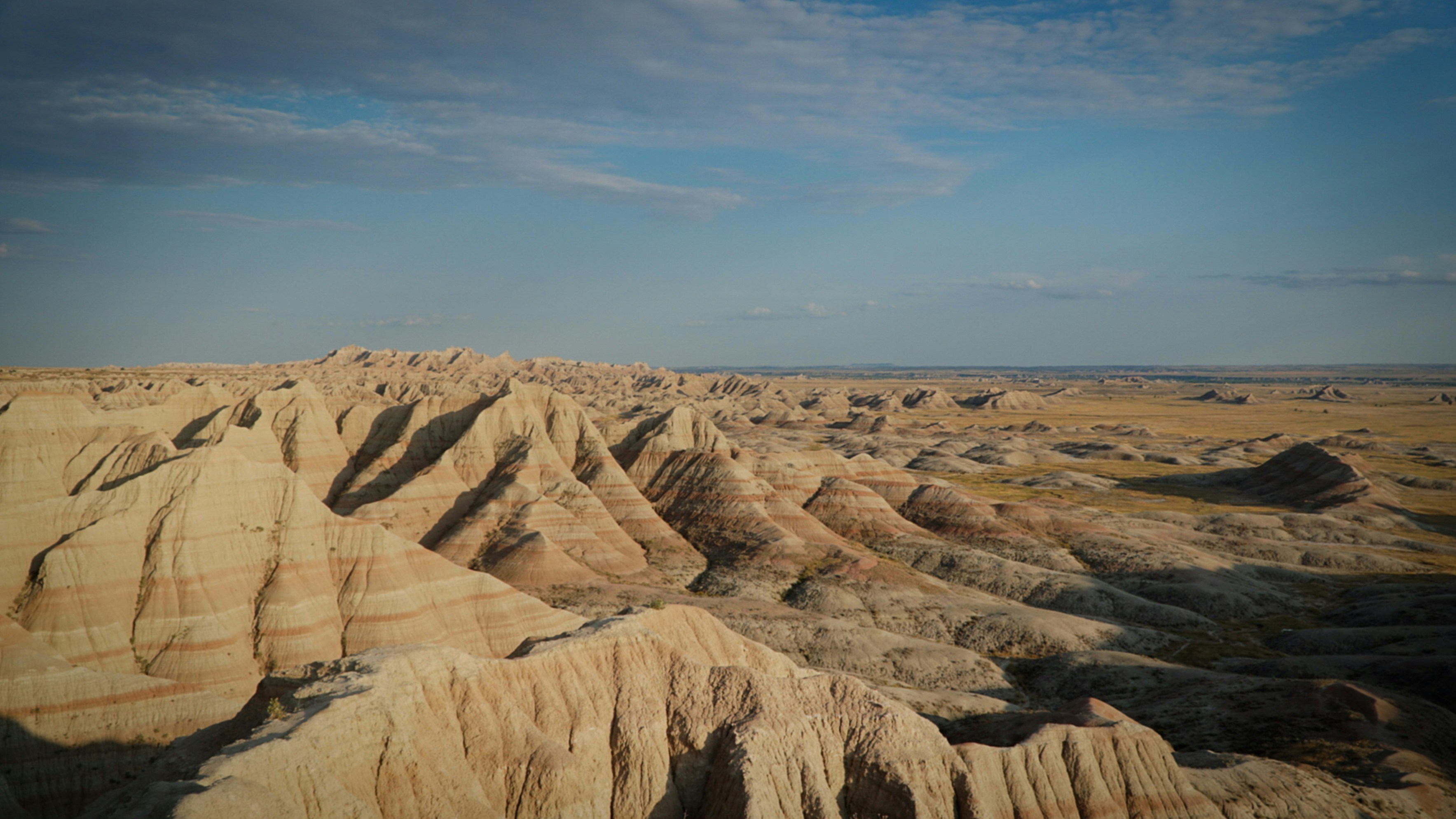 Vast Badlands landscape showcasing layered rock formations under a clear sky. The undulating terrain reveals the intricate patterns of nature's artistry.