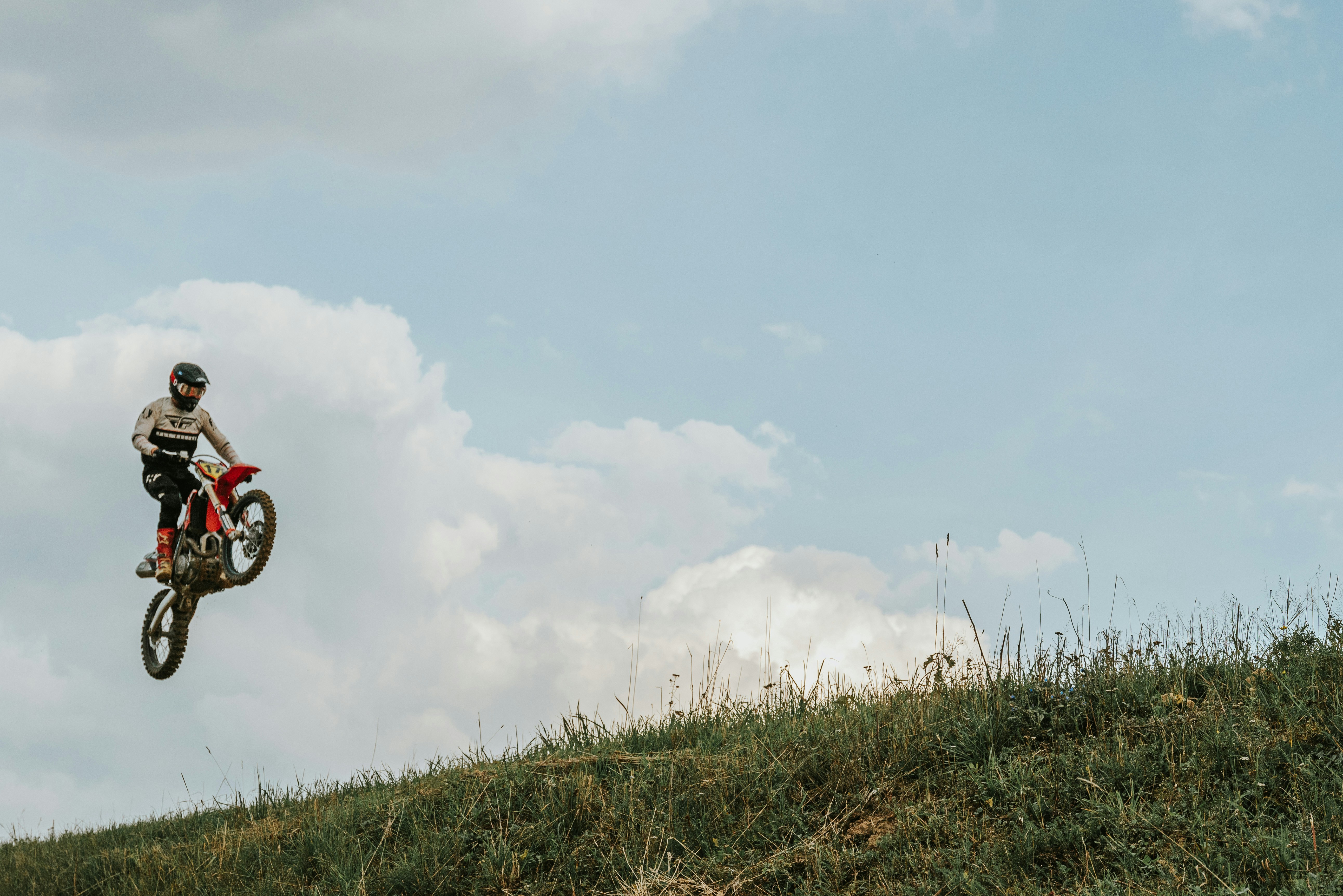 Motocross rider airborne above a grassy hill, showcasing dynamic movement against a backdrop of clouds.