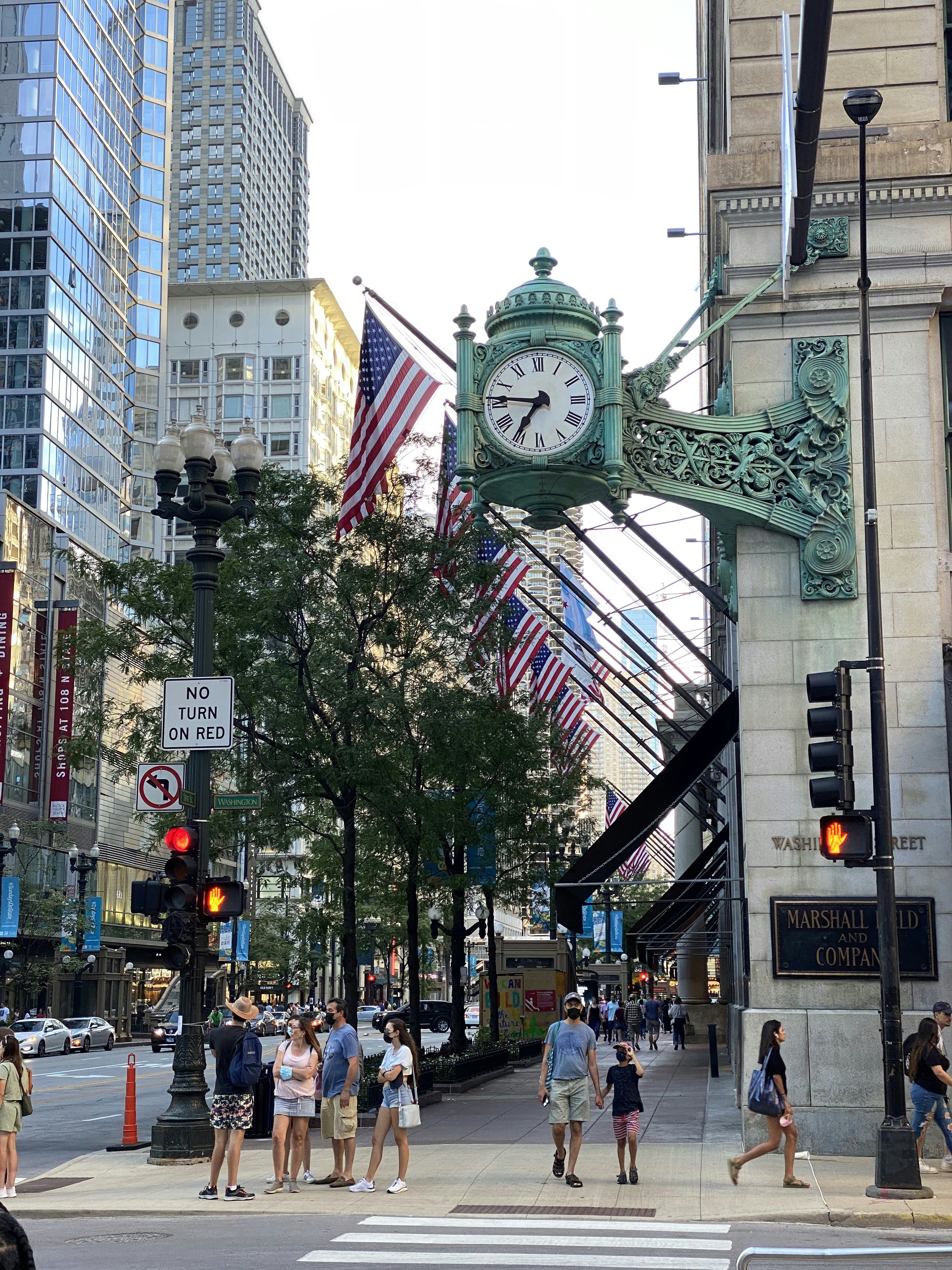 Historic clock adorned with intricate green metalwork, surrounded by American flags and bustling city life on State Street.