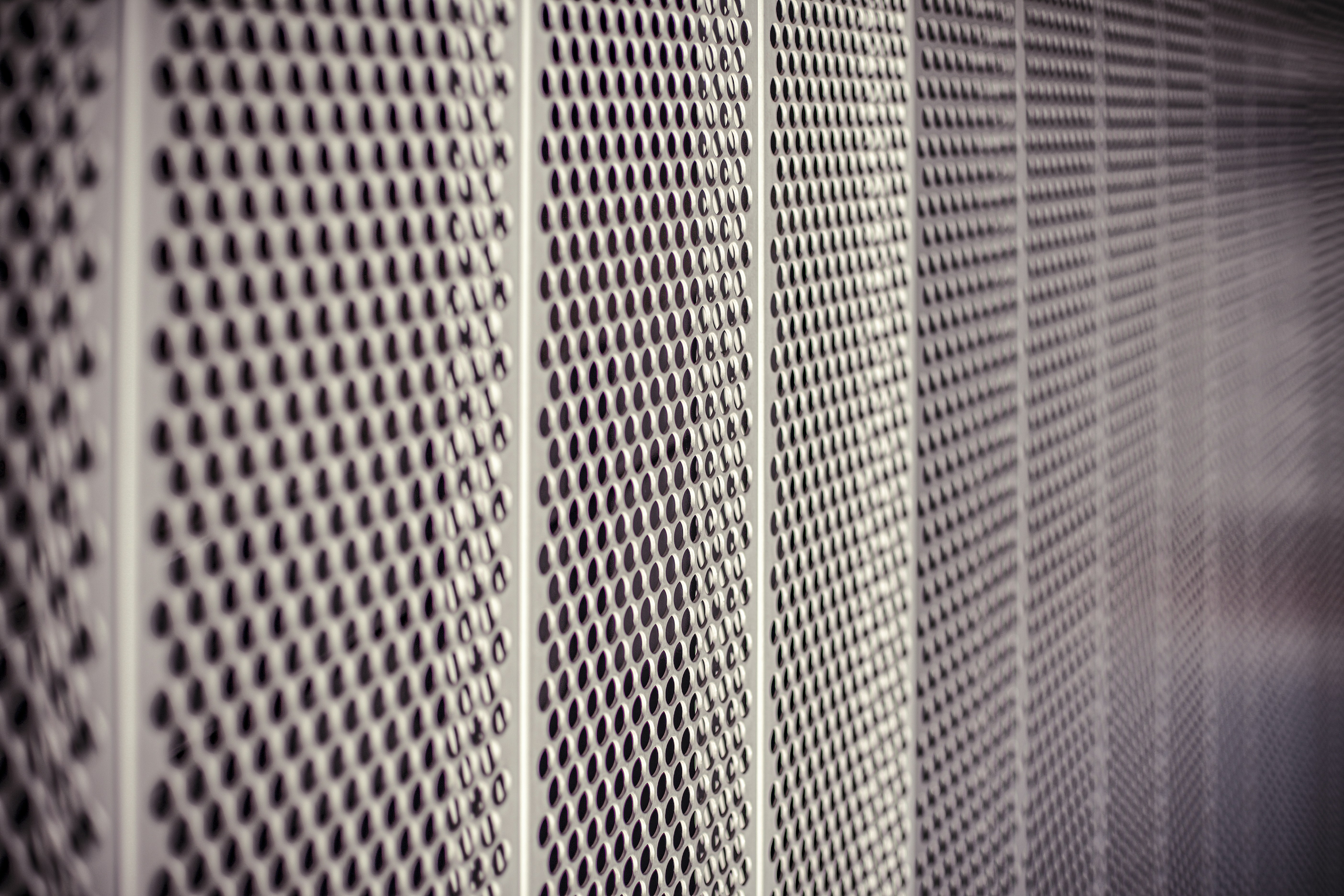 Close-up of a perforated metal panel showcasing intricate patterns and textures. The design highlights the interplay of light and shadow across the surface.
