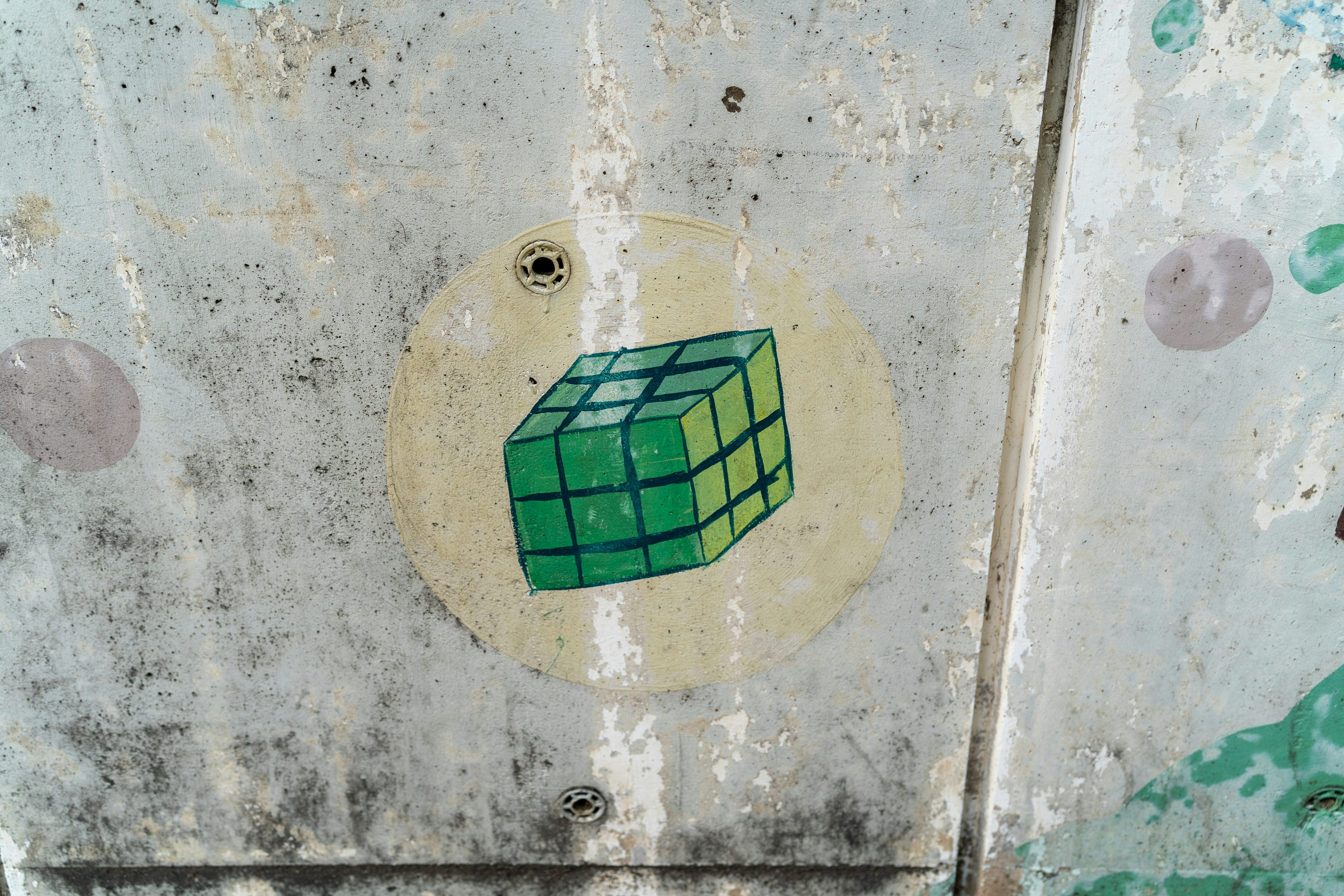 A weathered mural featuring a green Rubik's cube set against a faded background of peeling paint and grime.
