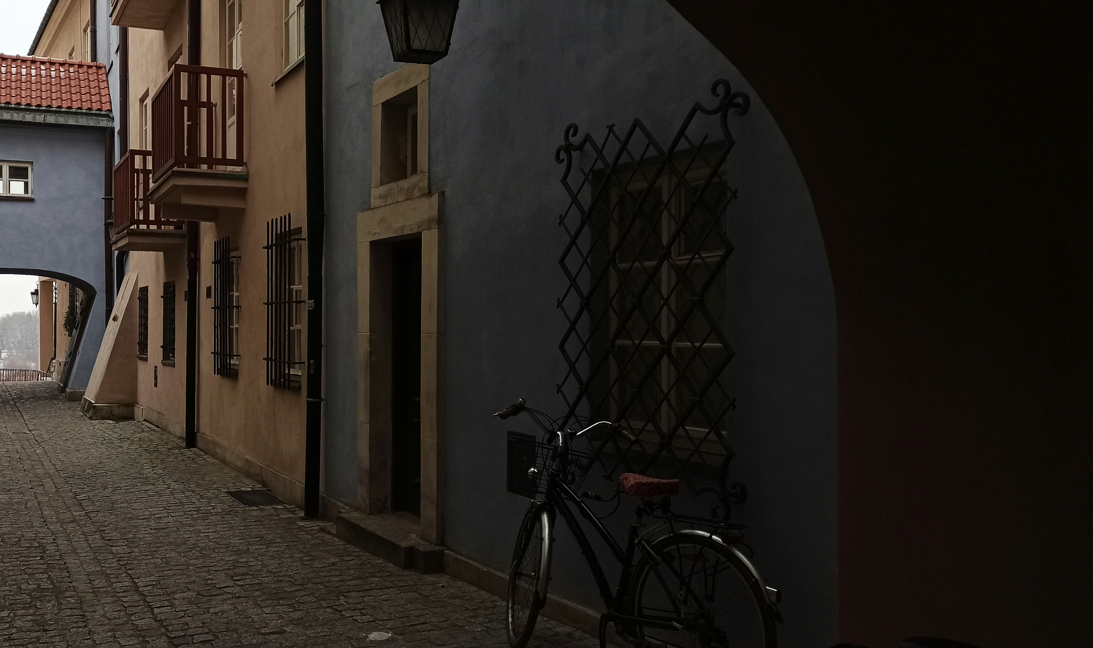 Narrow cobblestone alleyway bordered by pastel-colored buildings, featuring a vintage bicycle parked beside a textured wall.