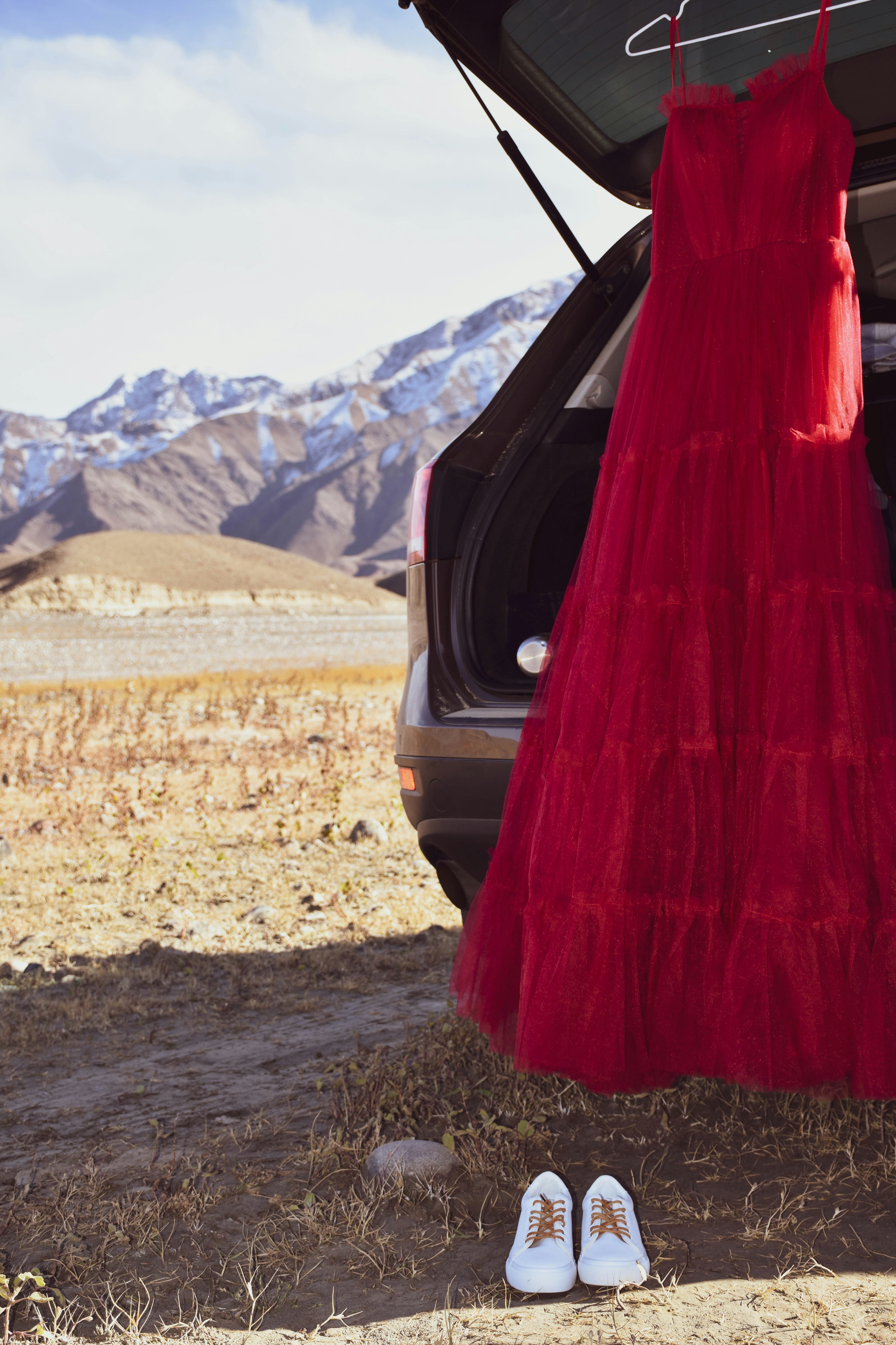 Crimson Dress Draped from an Open Trunk Against a Desert Mountain Backdrop