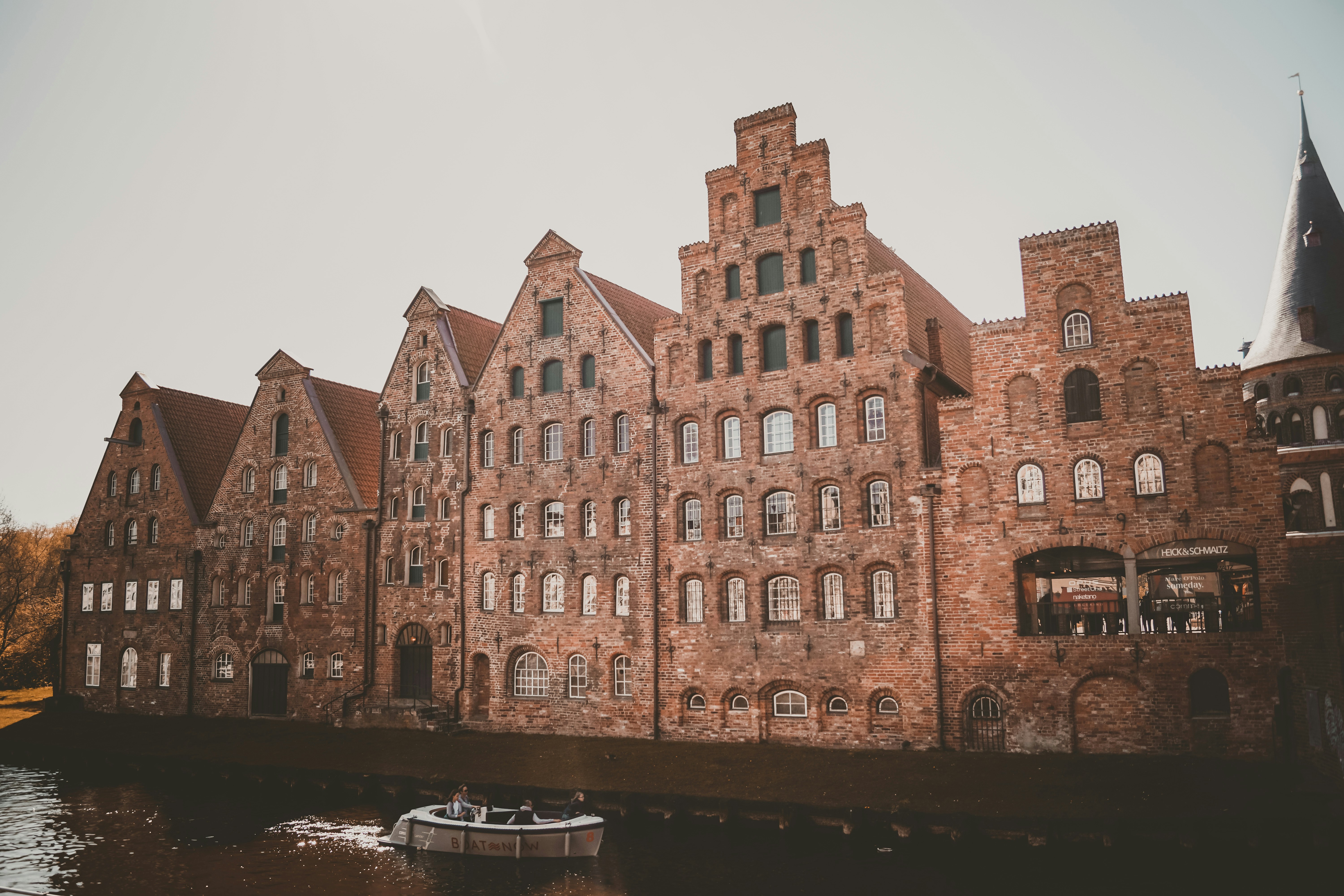 Row of brick buildings with stepped gables along a canal under a soft sky.