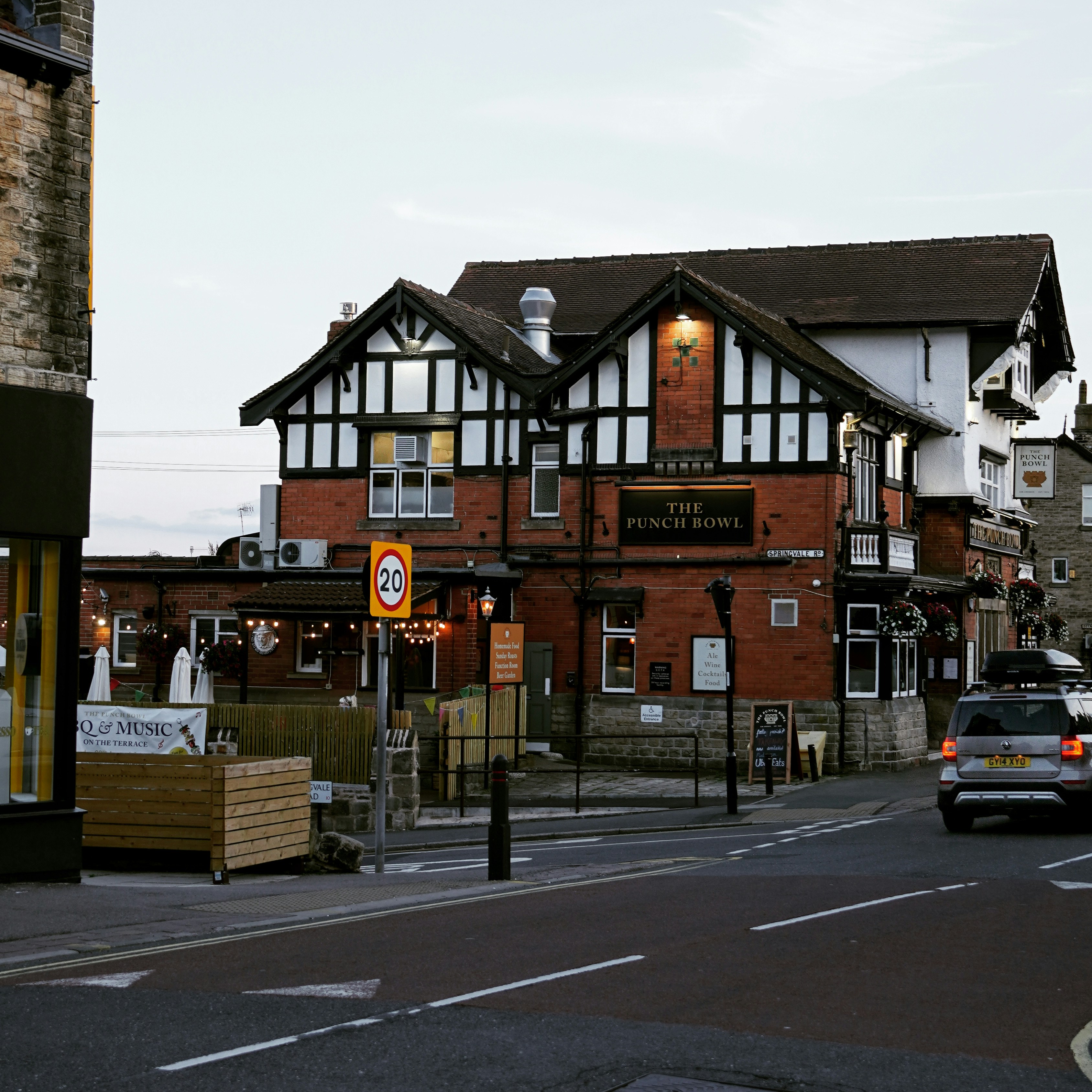 Traditional pub exterior illuminated by warm lights, set against a twilight sky. The scene captures the inviting atmosphere of a cozy gathering place.