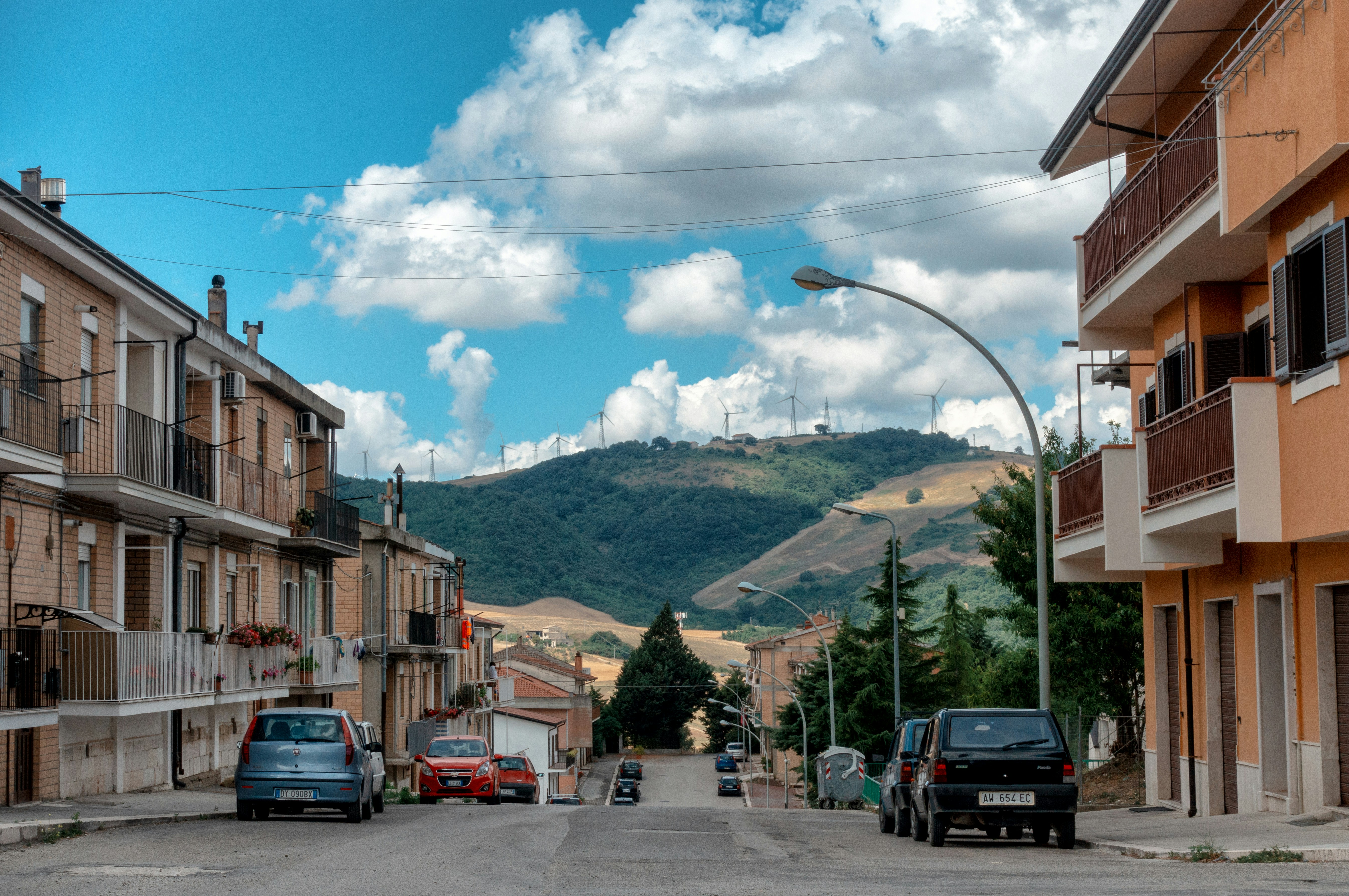 Quiet Italian street framed by colorful buildings and distant hills under a vibrant sky.