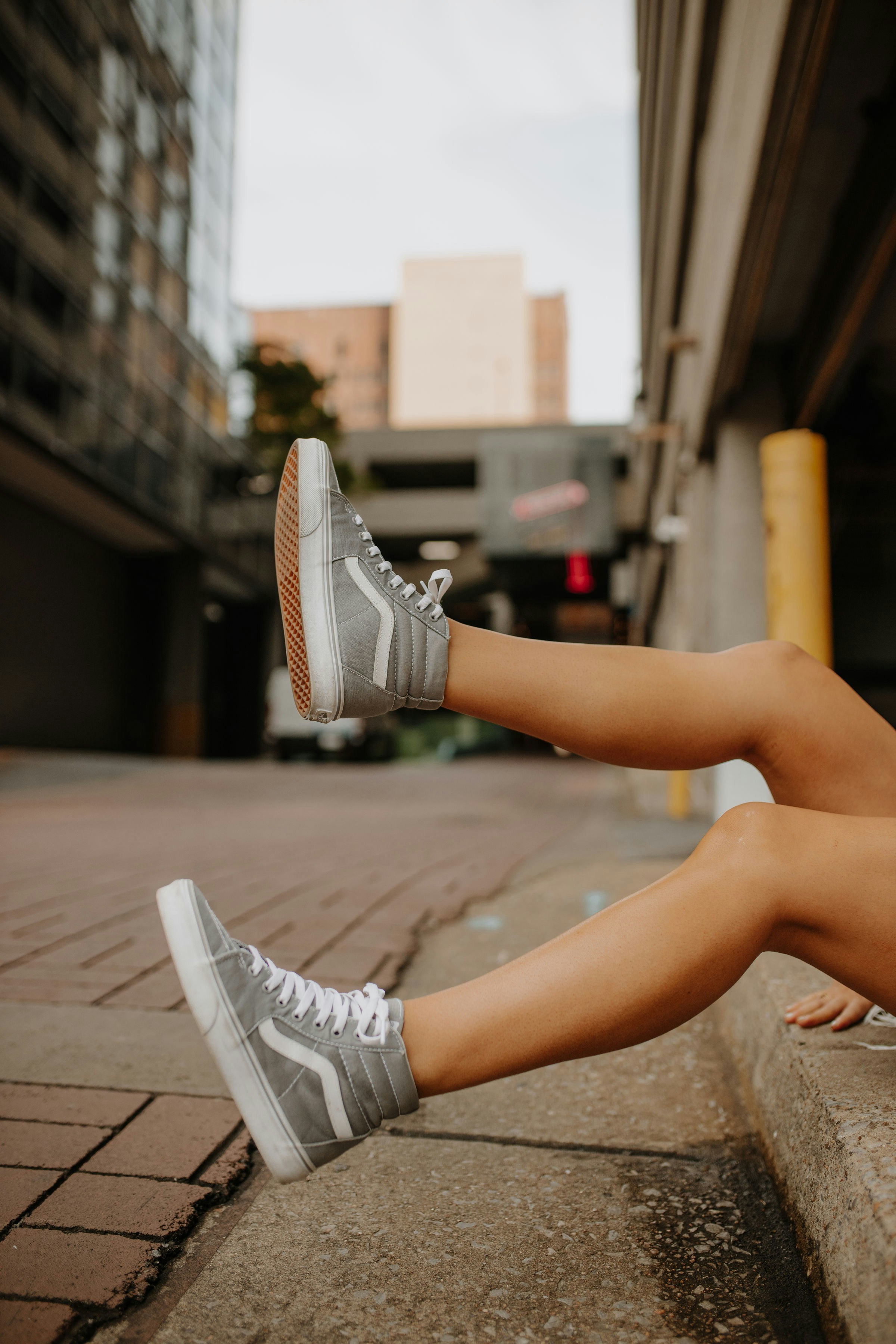 A pair of stylish high-top sneakers resting on the edge of a sidewalk in an urban setting, with city buildings blurred in the background.