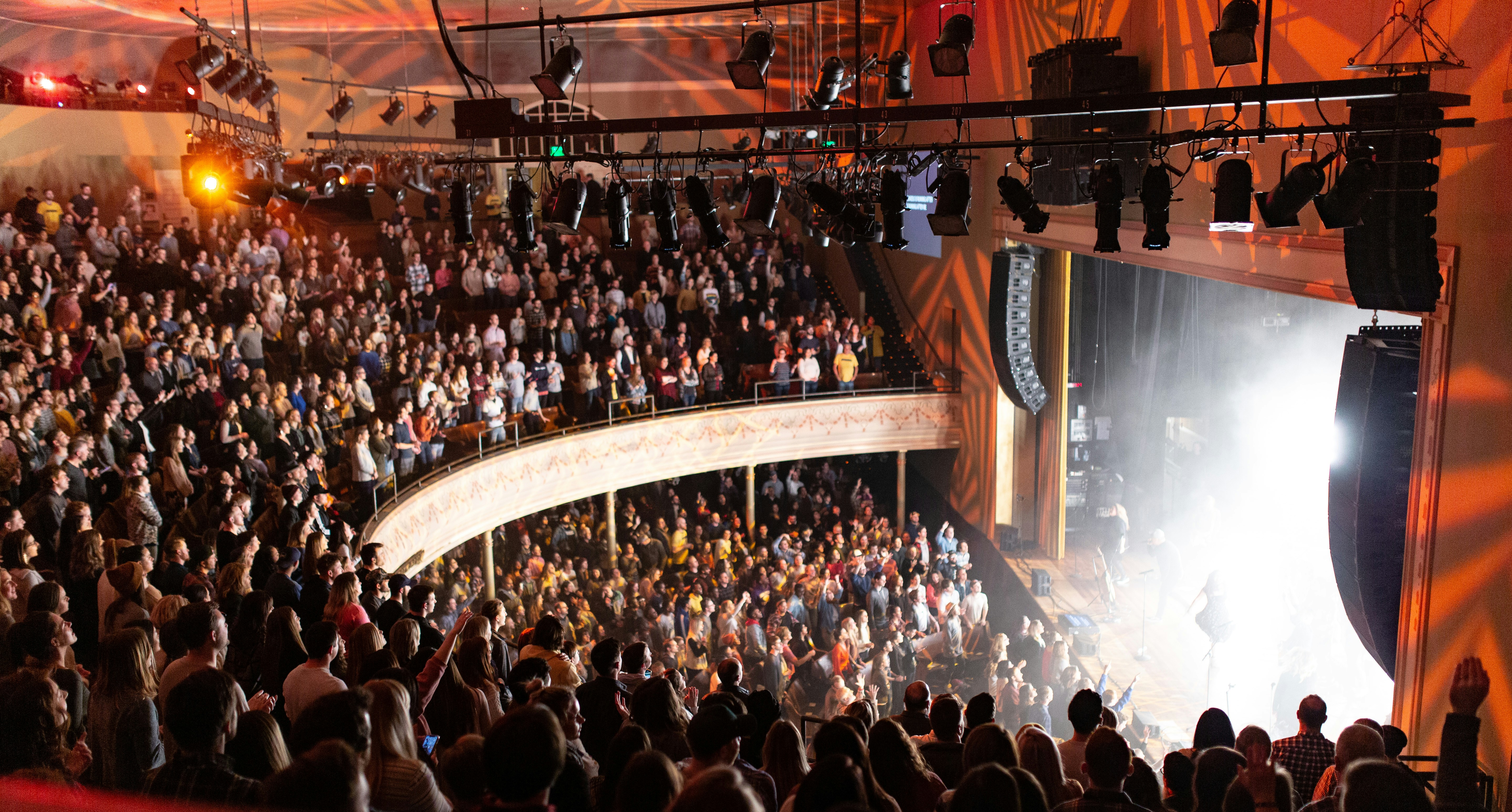 Large audience filling an auditorium with a spotlight illuminating the stage.