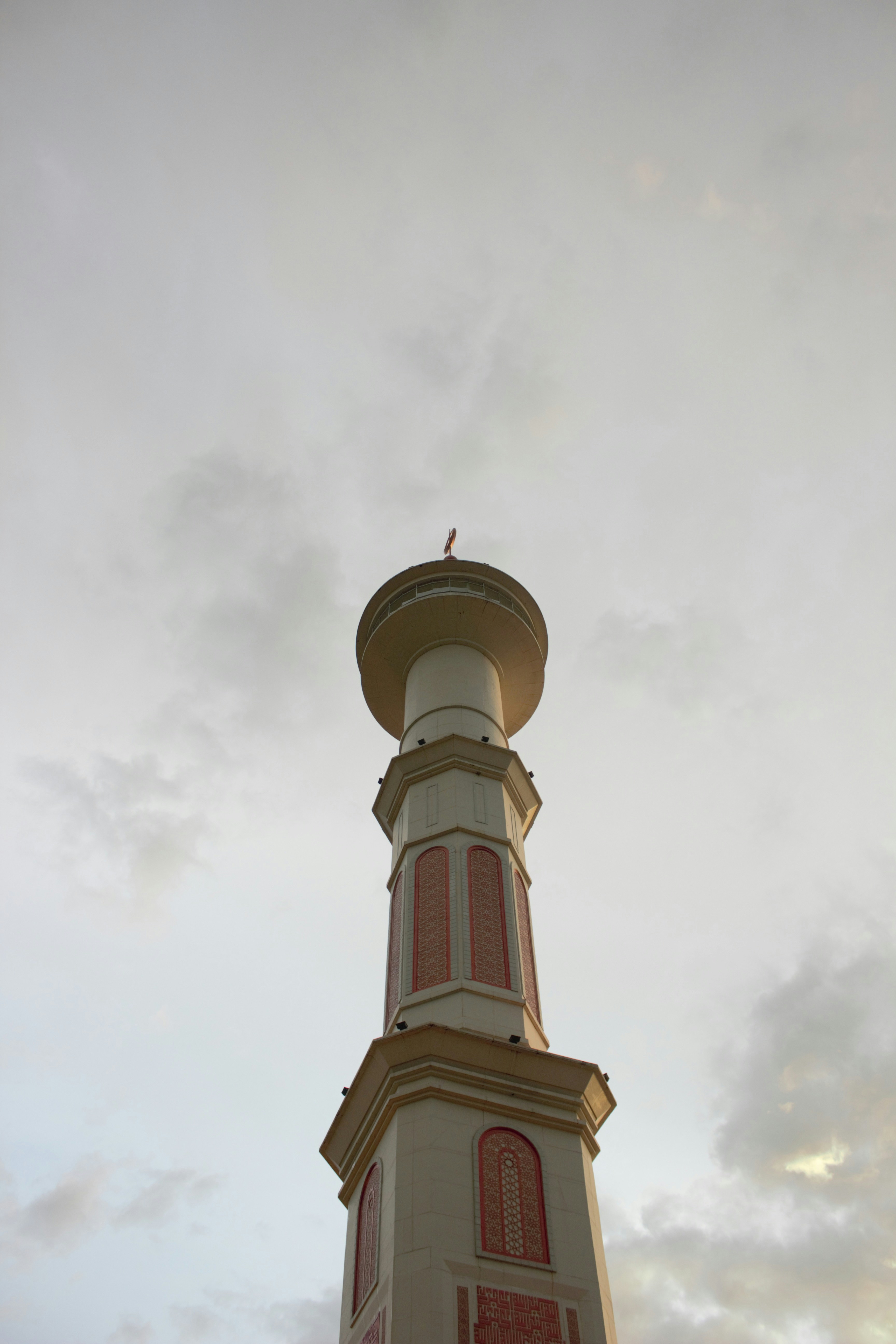 A tall minaret rises against a backdrop of soft, cloudy skies, showcasing intricate architectural details.