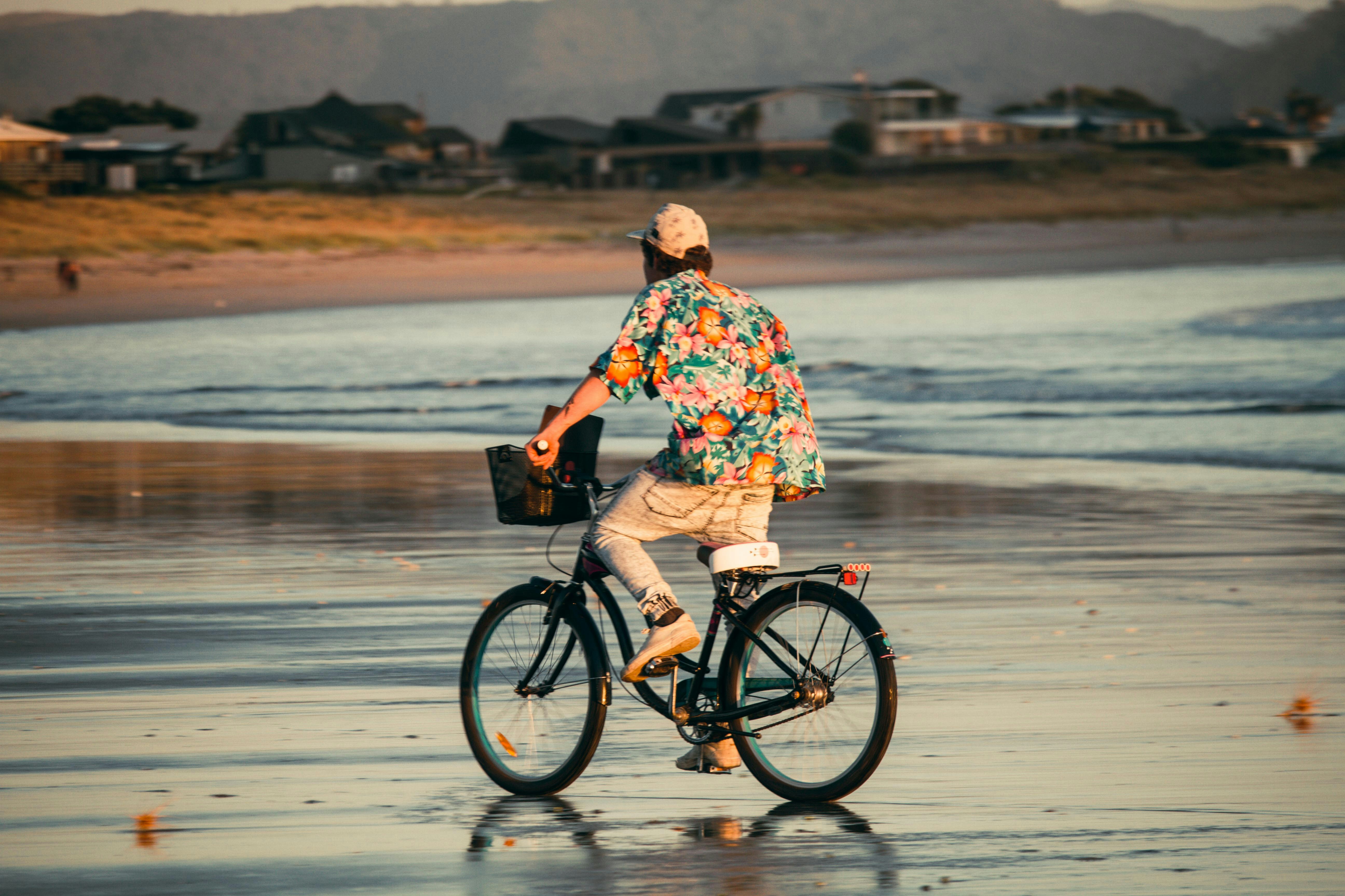 A man riding a bike down a beach next to the ocean photo – Free Biking ...