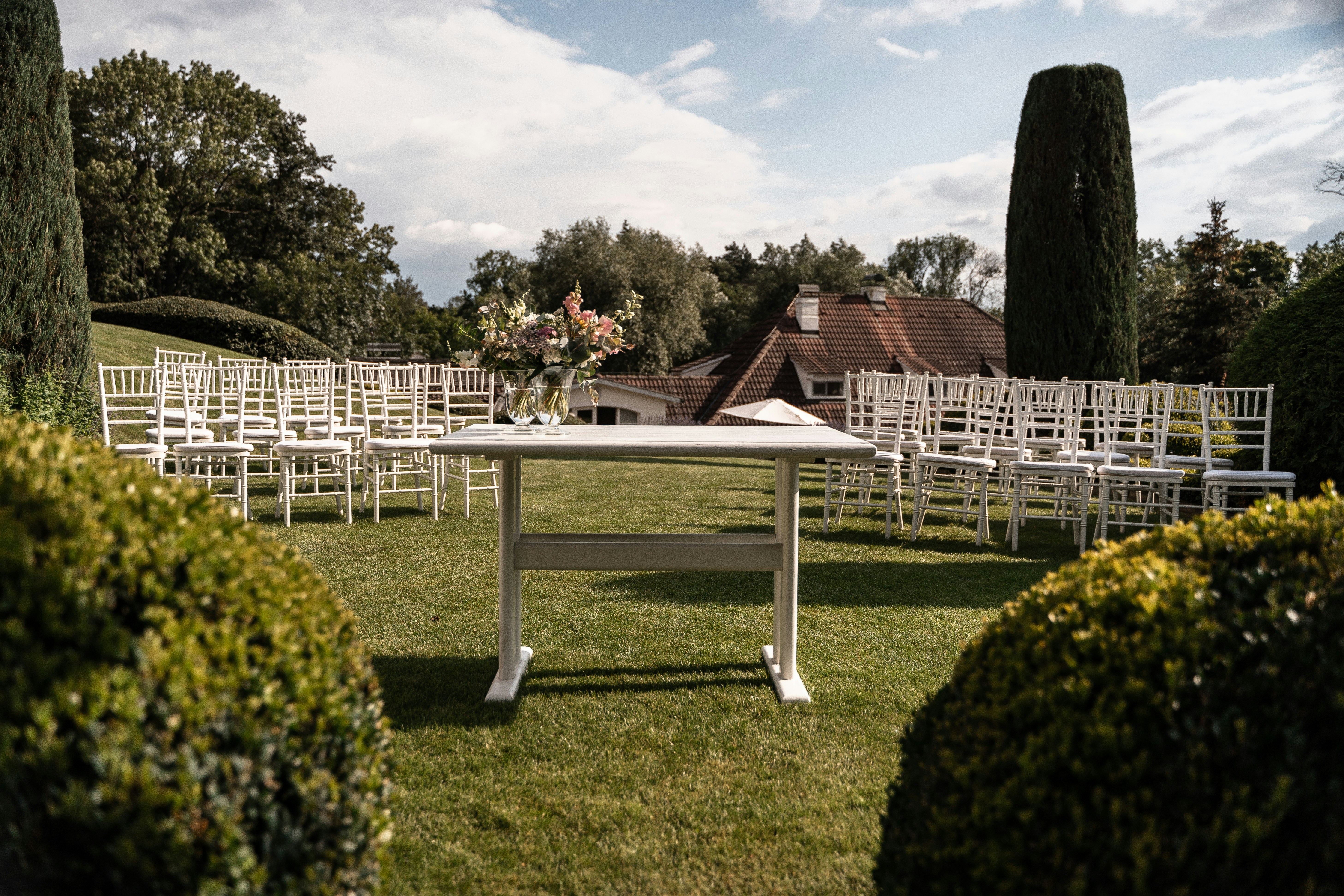 Central Ceremony Table Framed by White Chairs in a Sunlit Garden