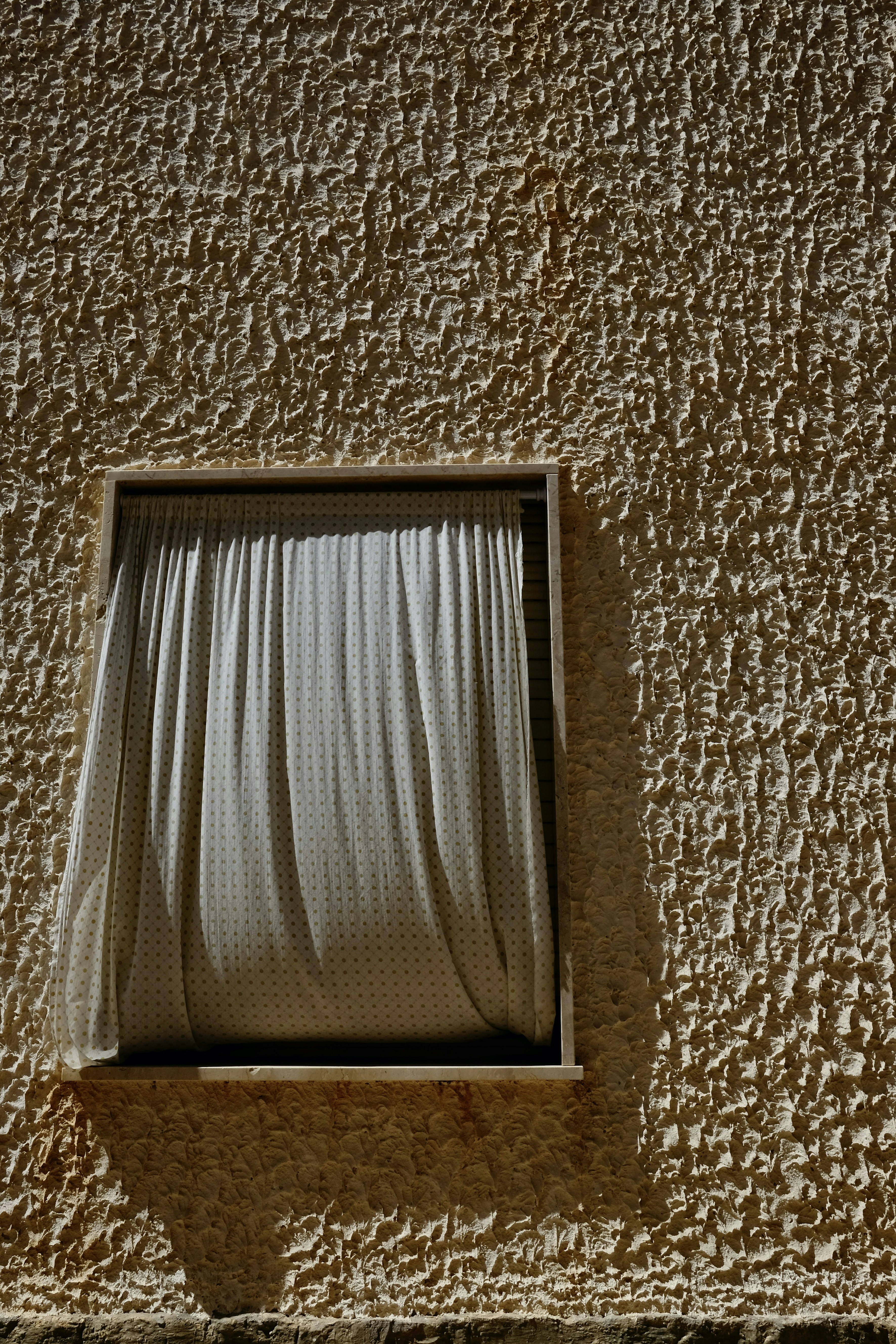A softly draped curtain in a textured wall, hinting at the life within while casting gentle shadows. 