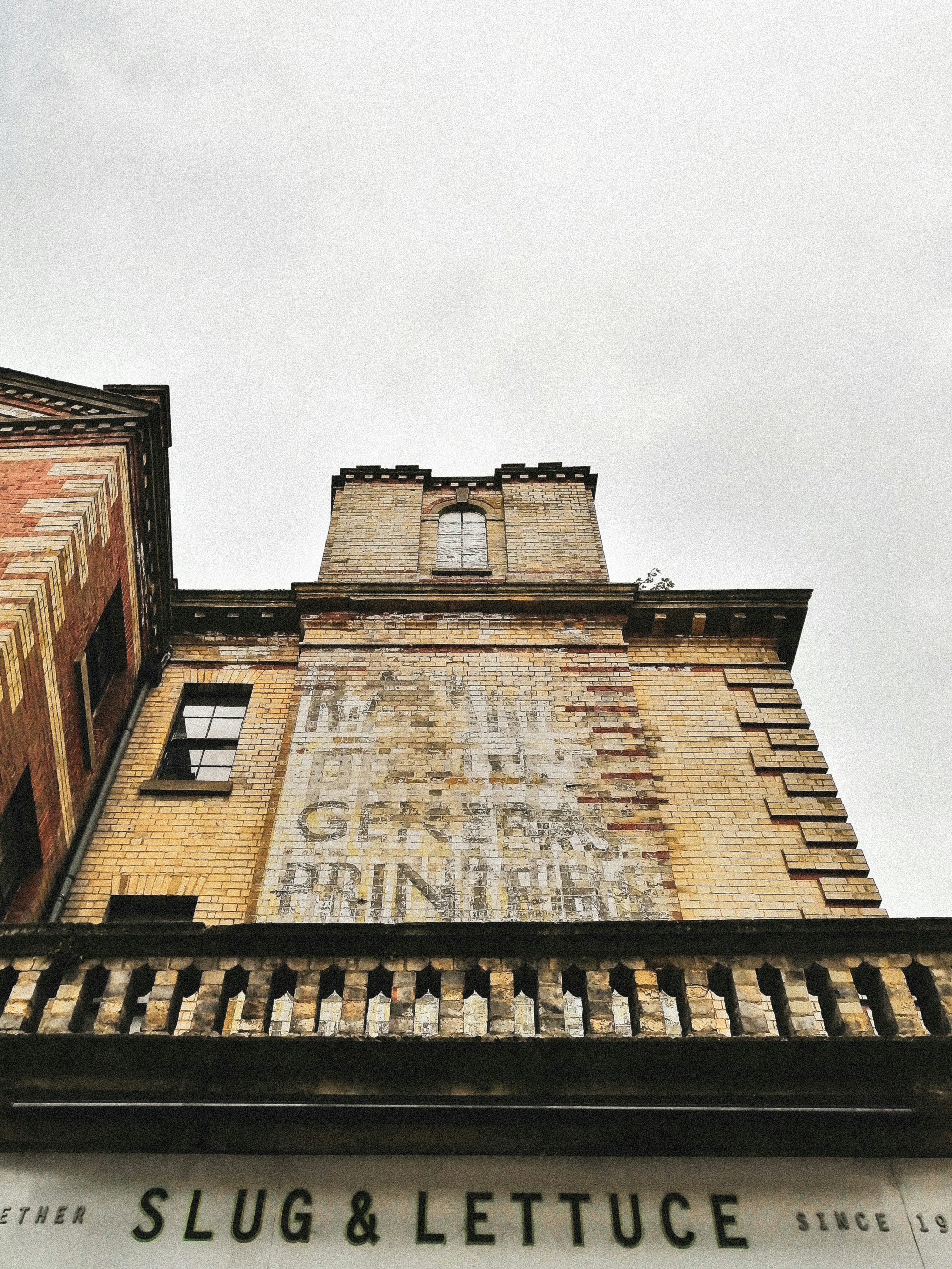 Looking up at a historic building with a weathered advertisement above a modern storefront.
