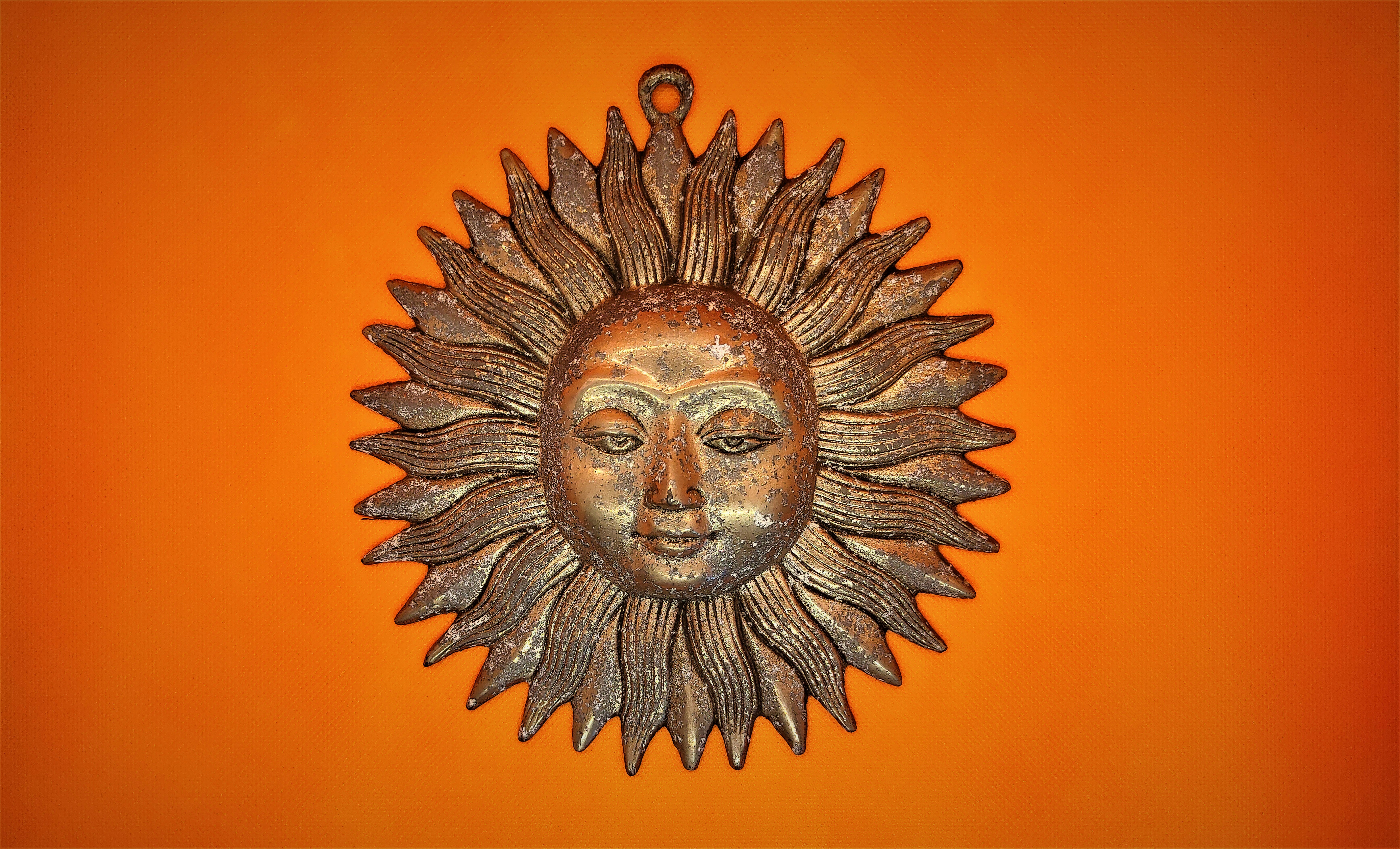 Intricately designed sun motif with a textured surface, set against a vibrant orange background.