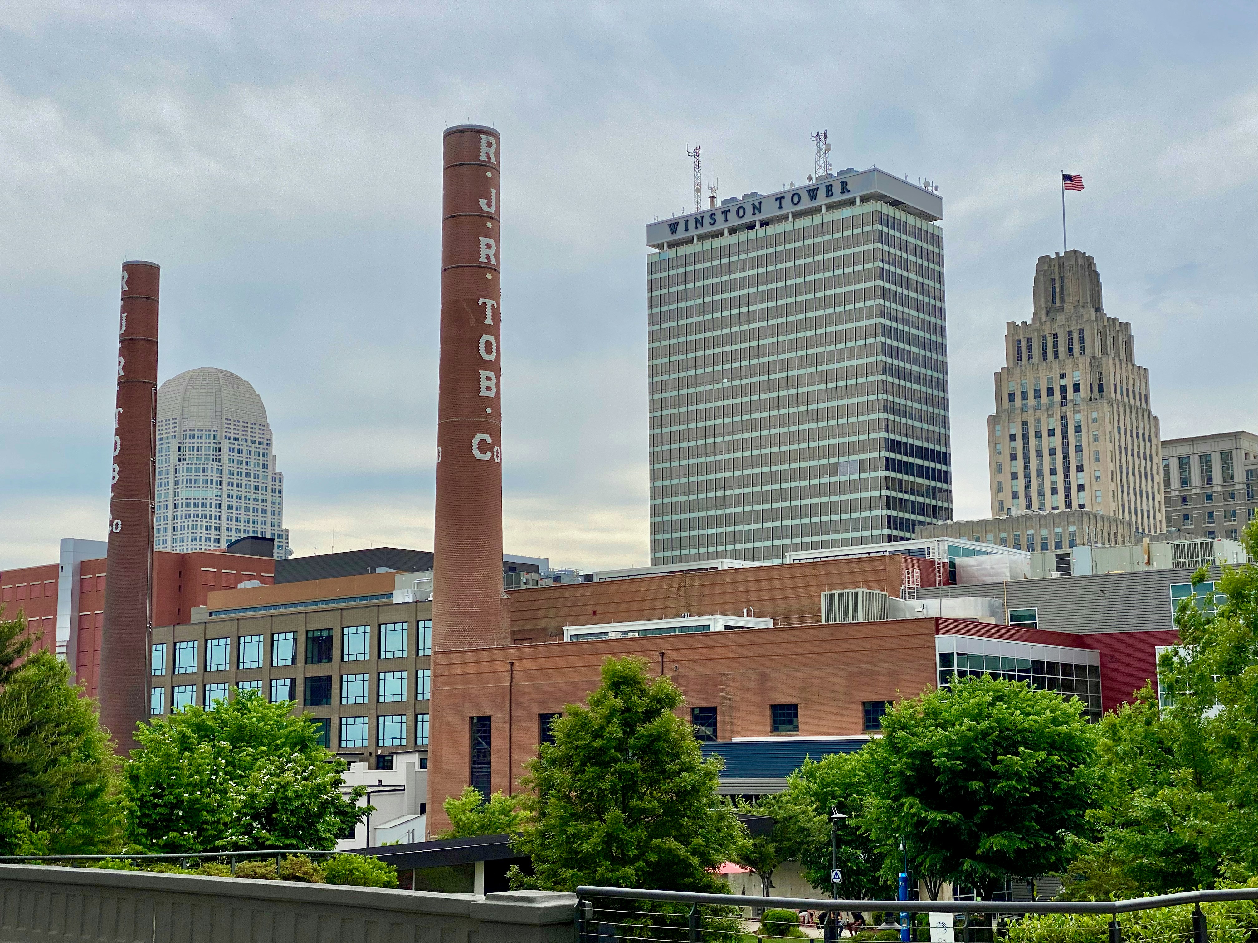 Historic smokestacks rise against a modern cityscape under a cloudy sky.