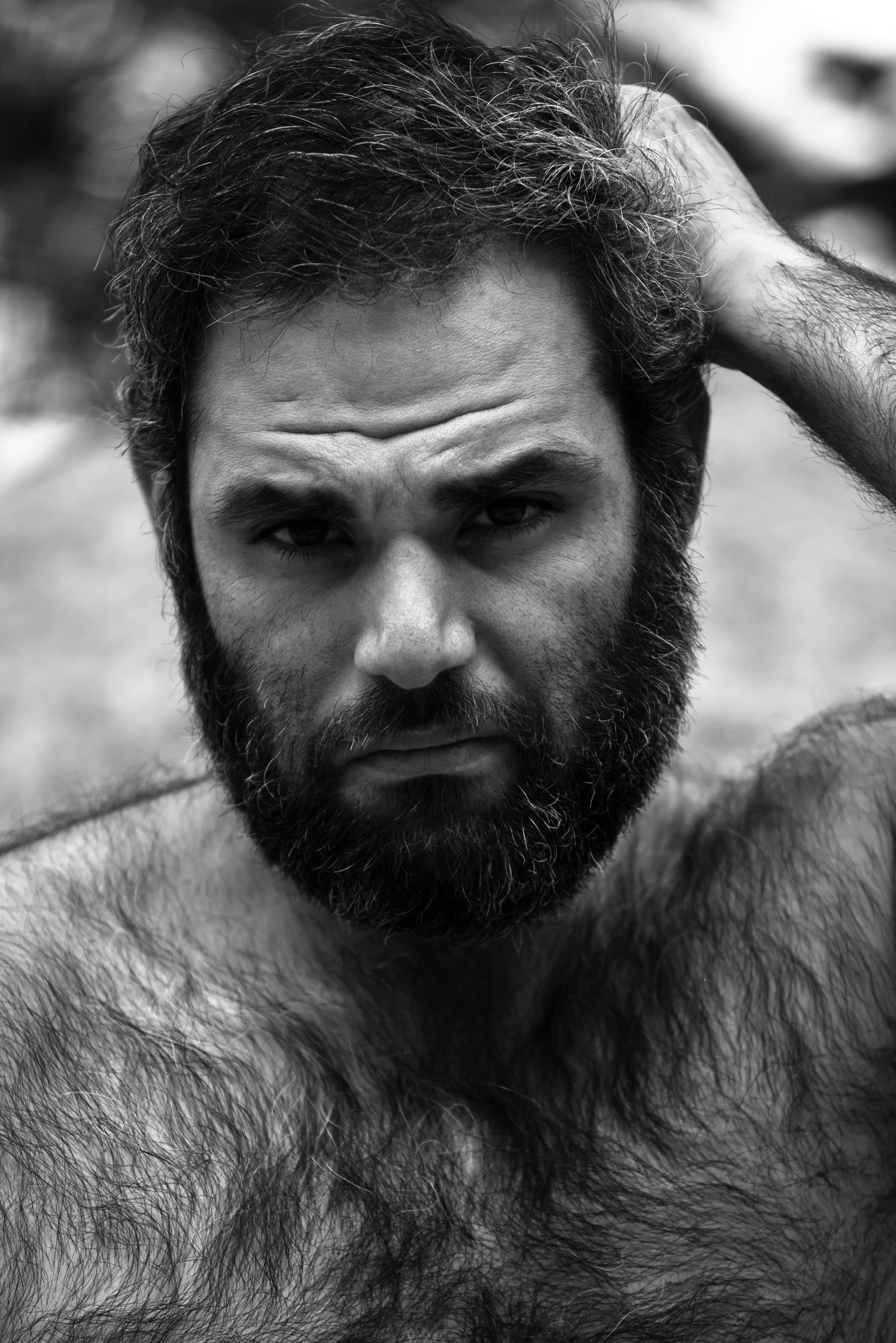 A rugged man with a contemplative expression, showcasing a thick beard and tousled hair, set against a blurred natural background.