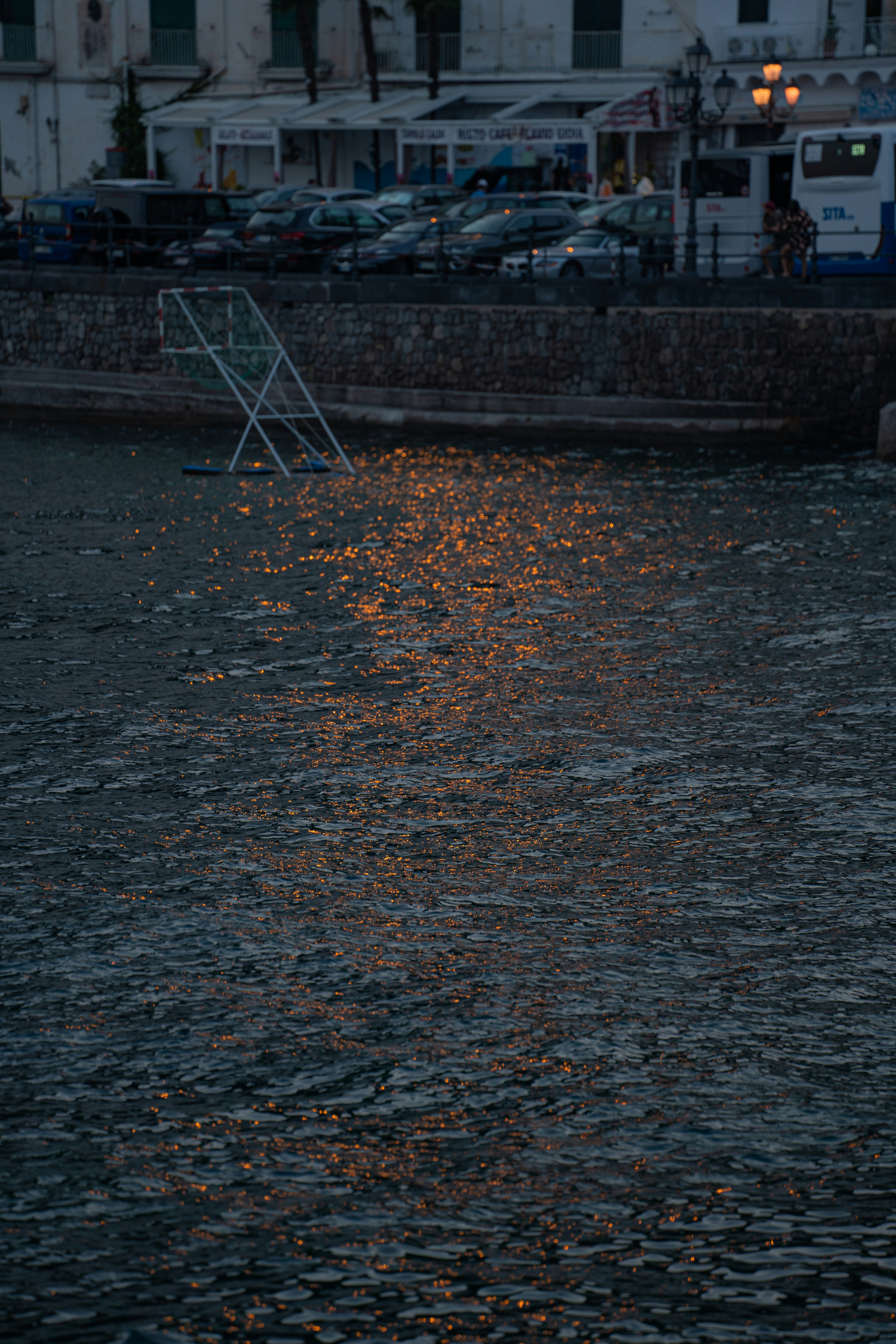 Soft evening light reflects on rippling water near a stone dock, with a ladder partially submerged.