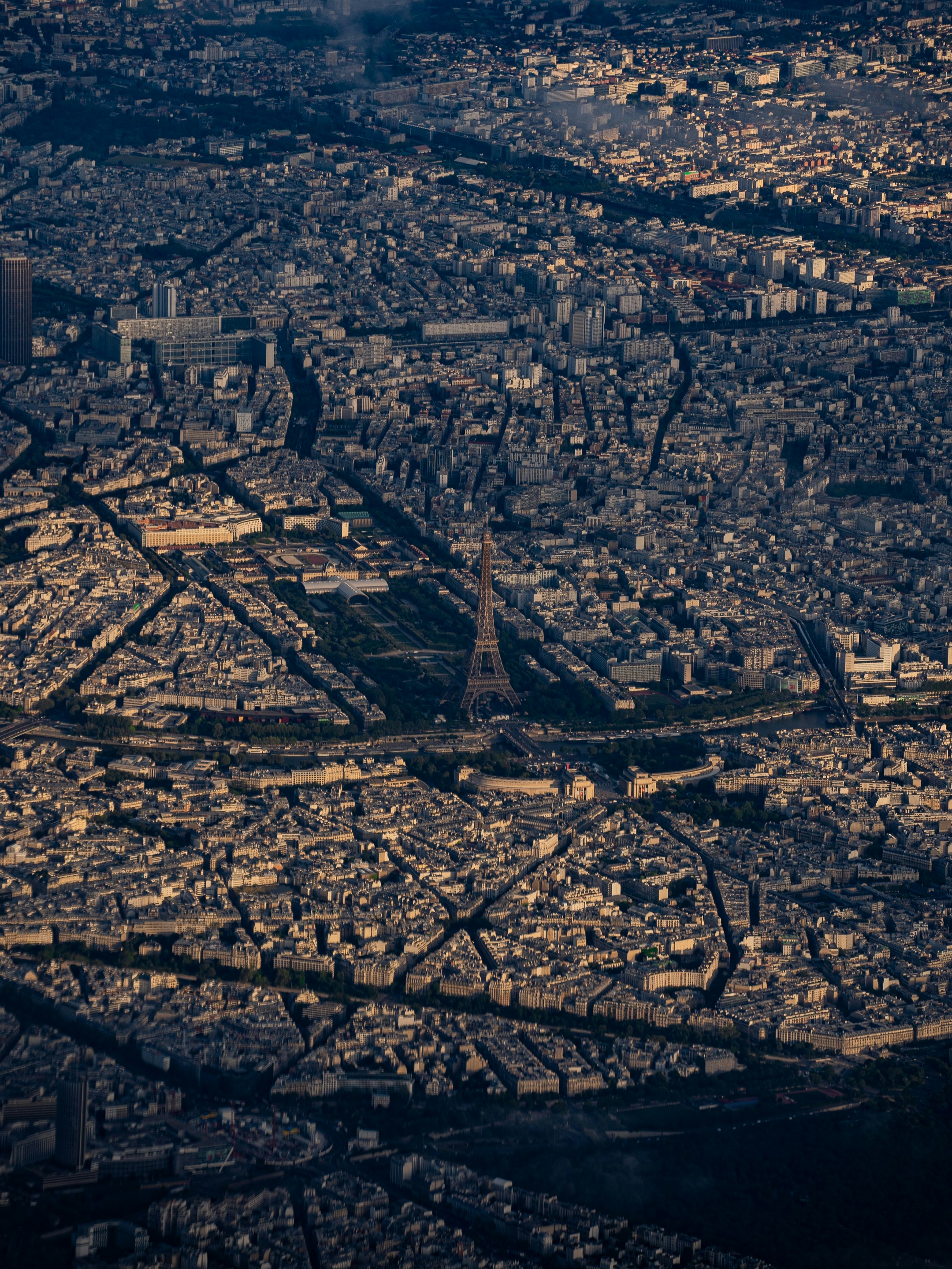 Aerial view showcasing the intricate layout of Paris, with the iconic Eiffel Tower prominently nestled among the cityscape. The contrast of urban structures against the lush greenery is striking.