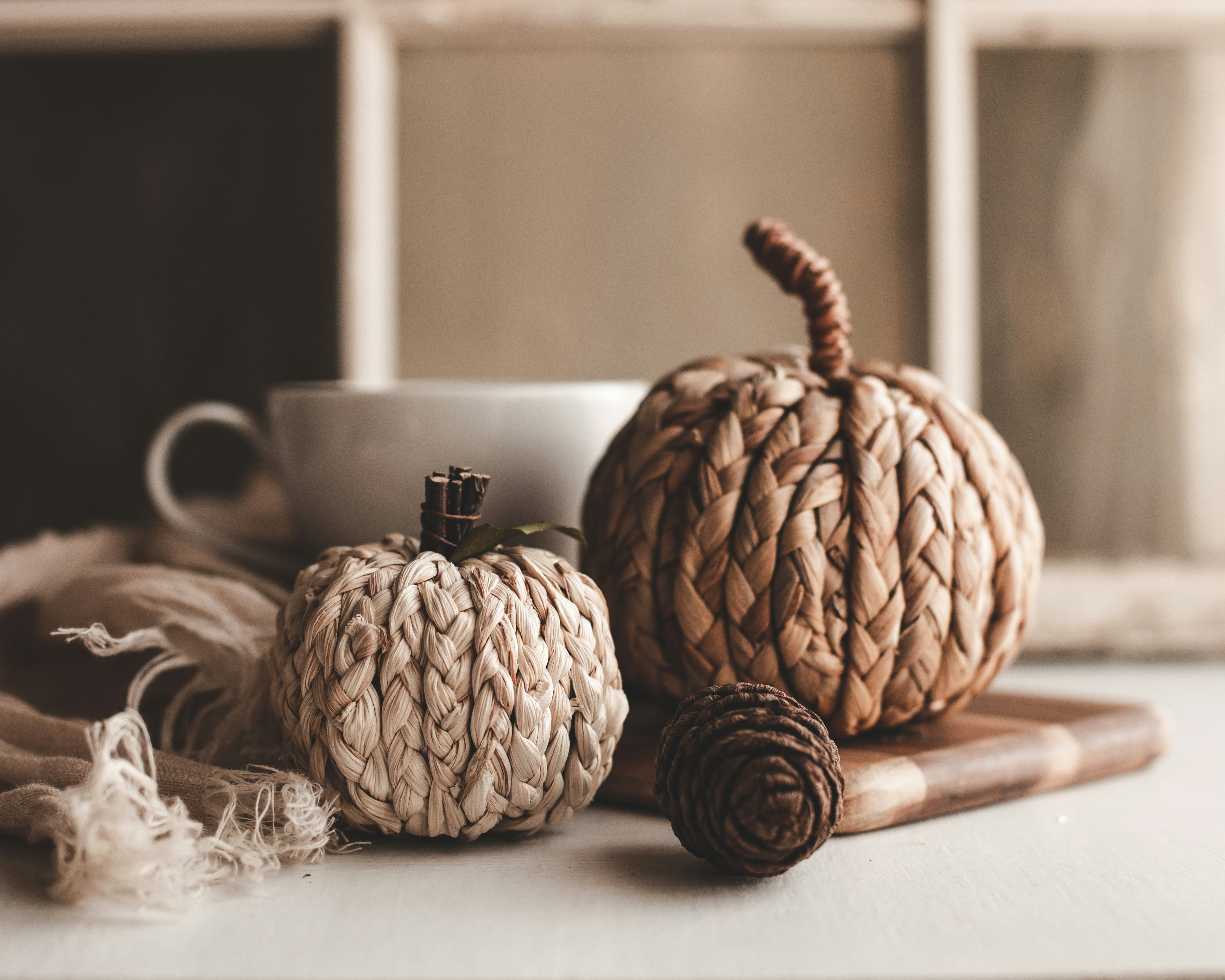 Woven pumpkins and a cup create a cozy autumn display on a wooden board.