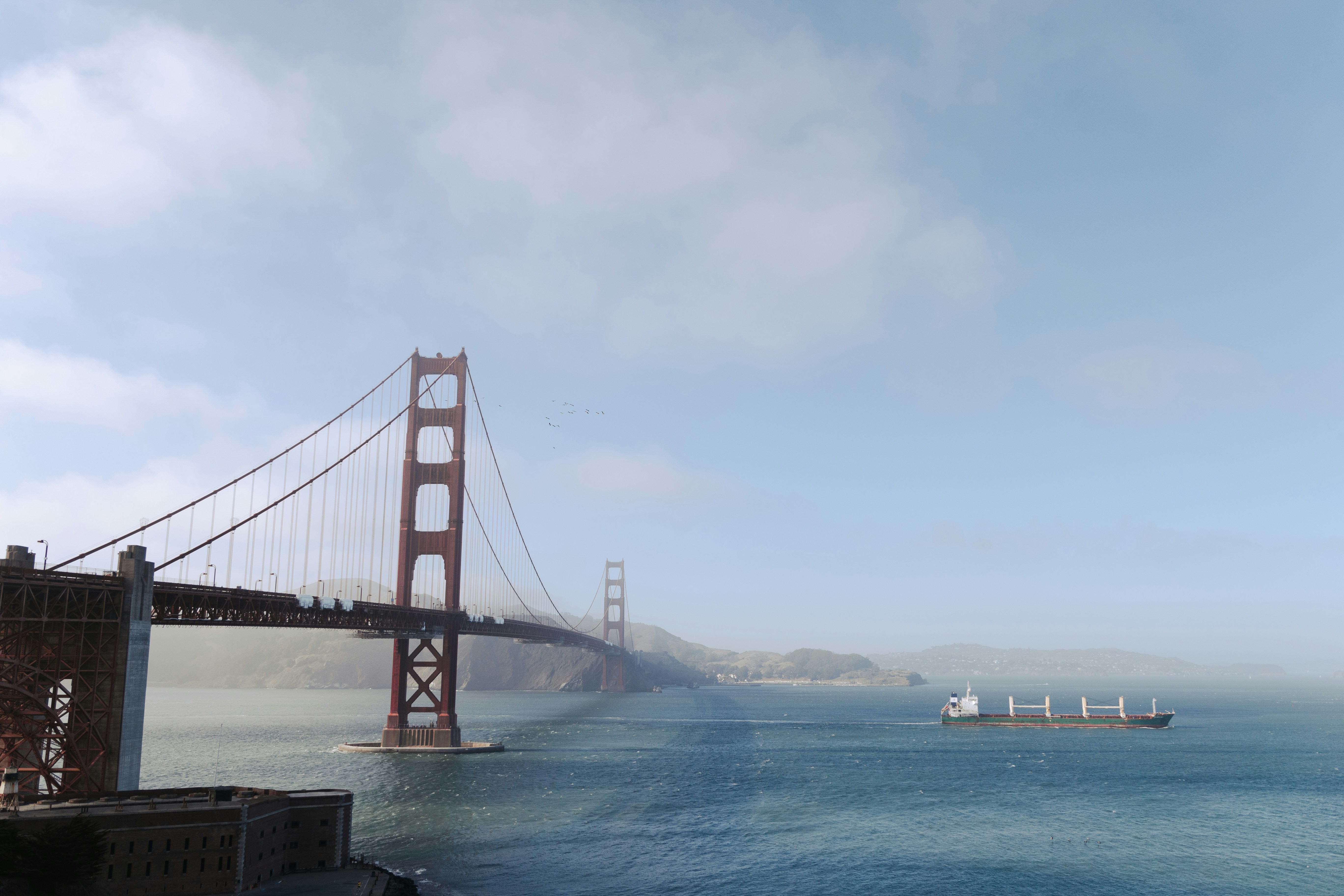 Golden Gate Bridge stretching across a foggy bay, with a cargo ship navigating the serene waters. 