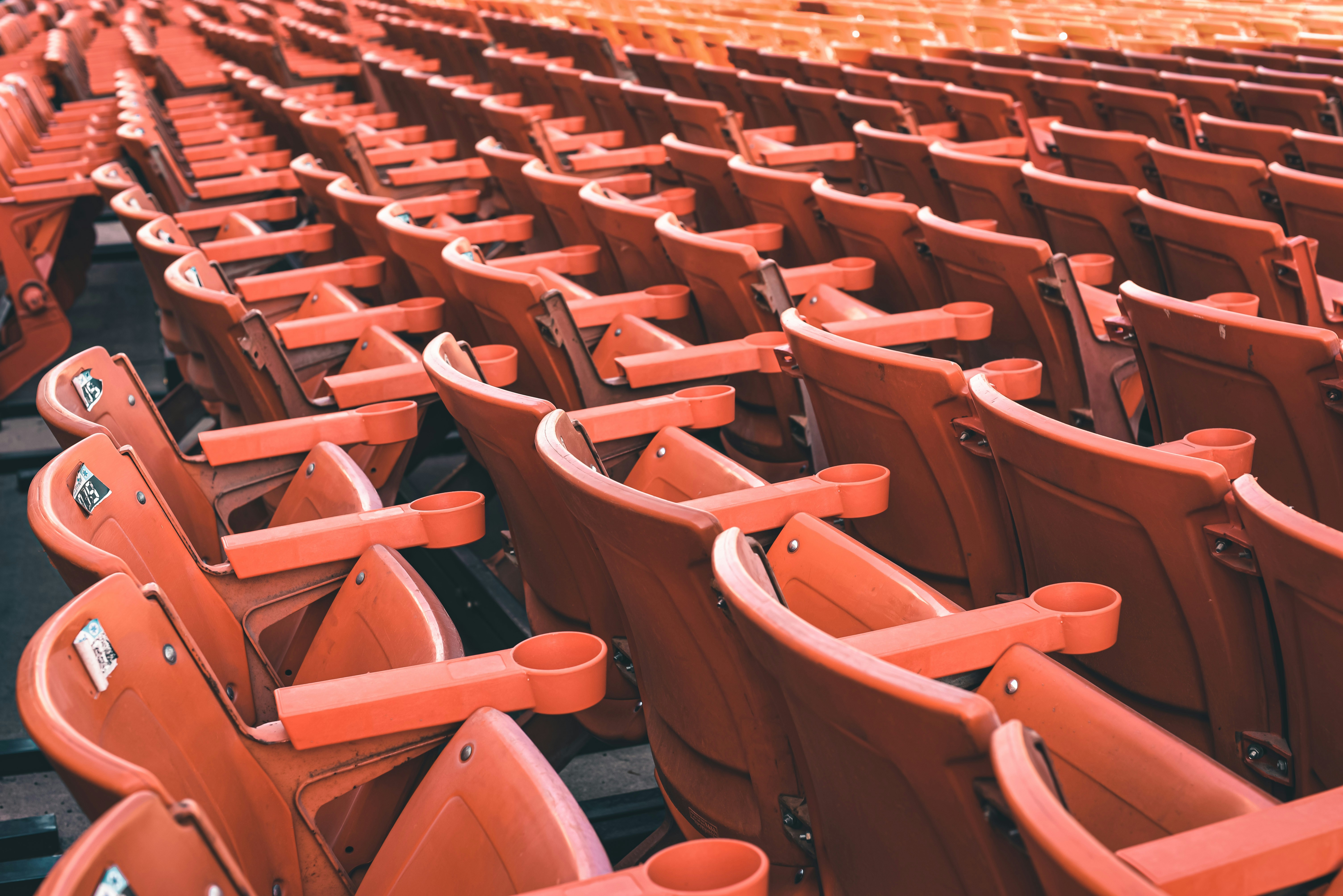 Rows of vibrant orange stadium seats create a rhythmic pattern, highlighting the absence of spectators. The image captures the essence of anticipation before an event.
