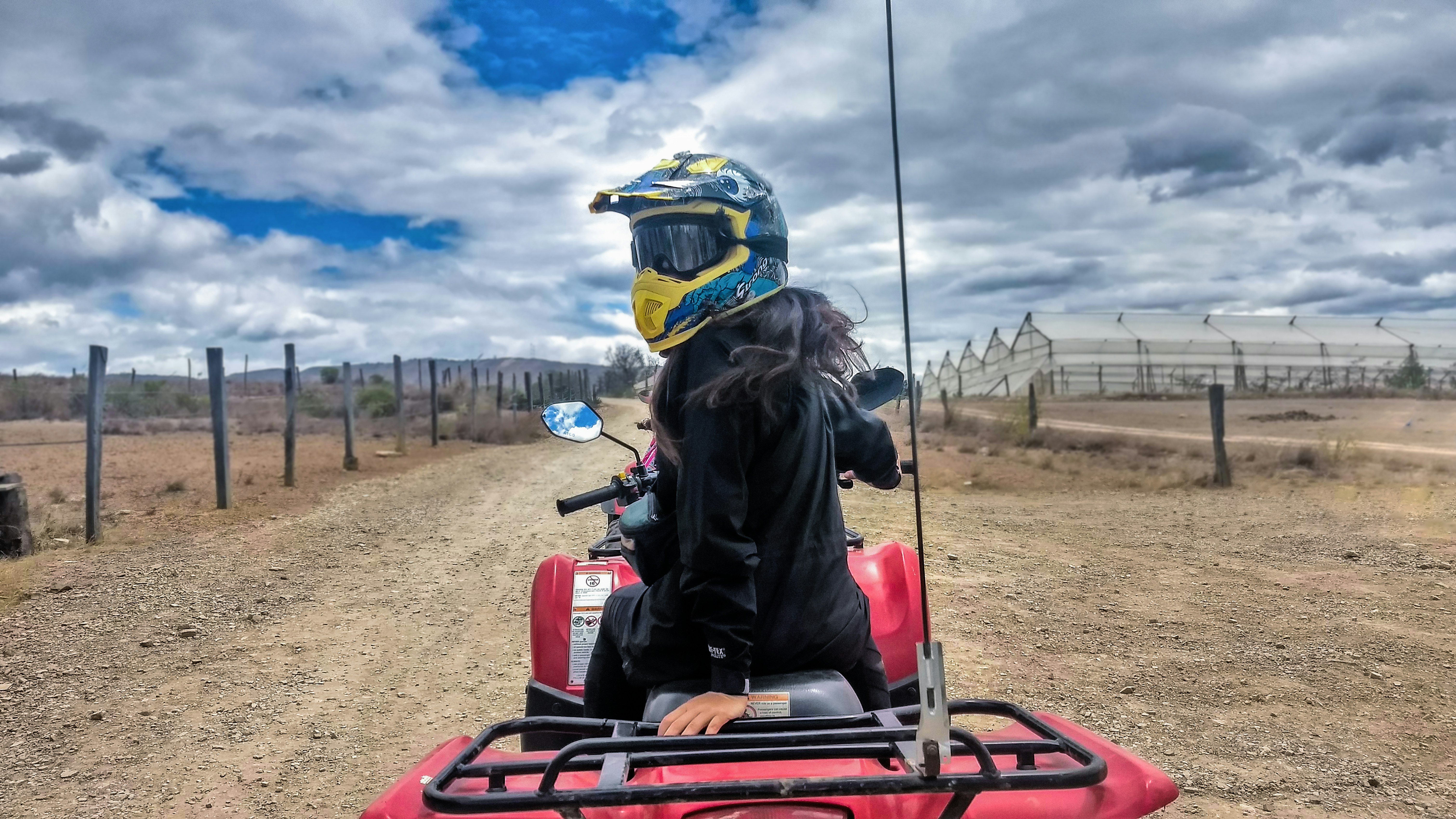 Person wearing a helmet sits on a red ATV on a dirt path under a cloudy sky.