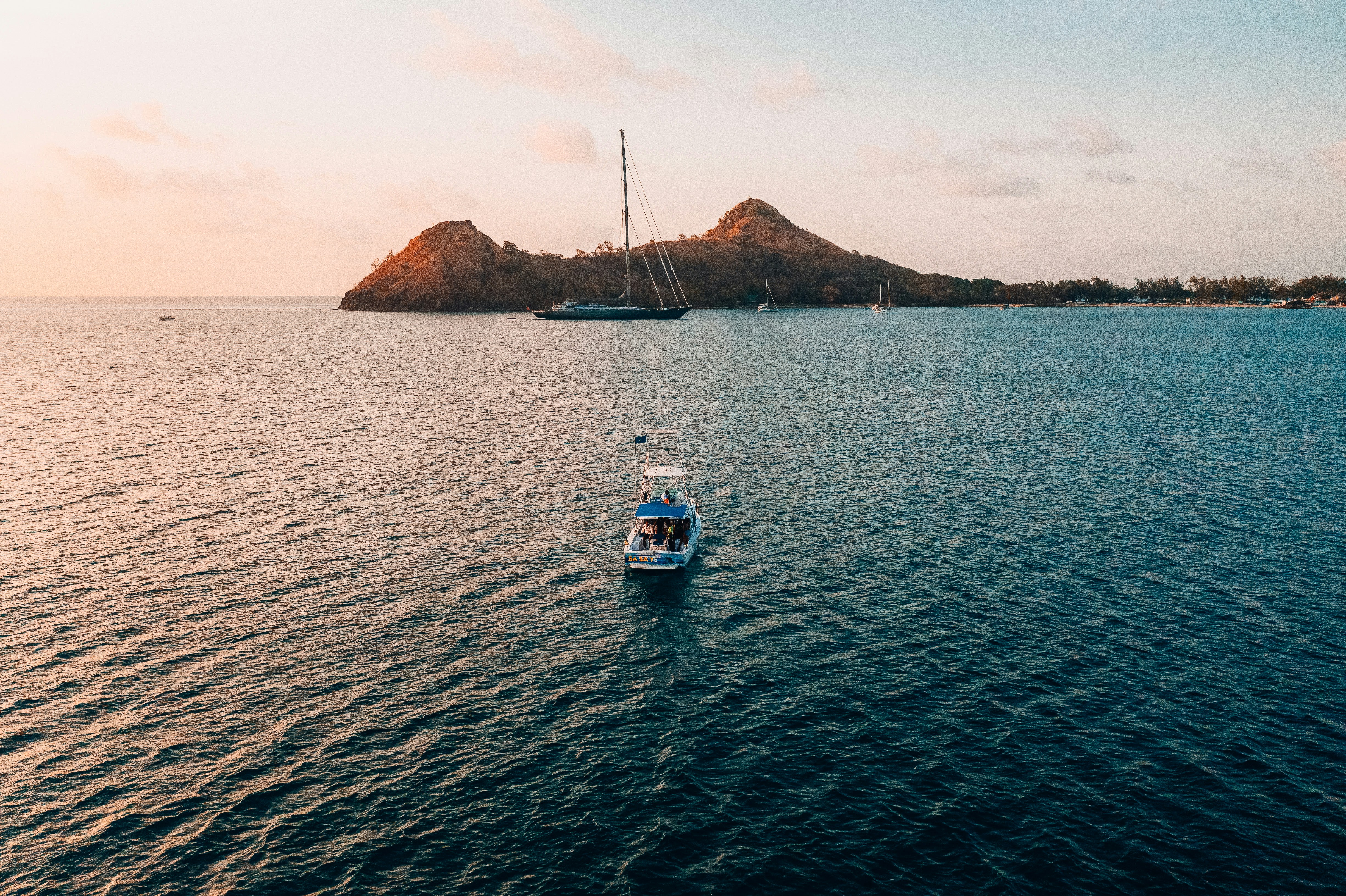 A boat gliding across calm waters with distant hills under a pastel sky. The scene captures a tranquil moment in nature.