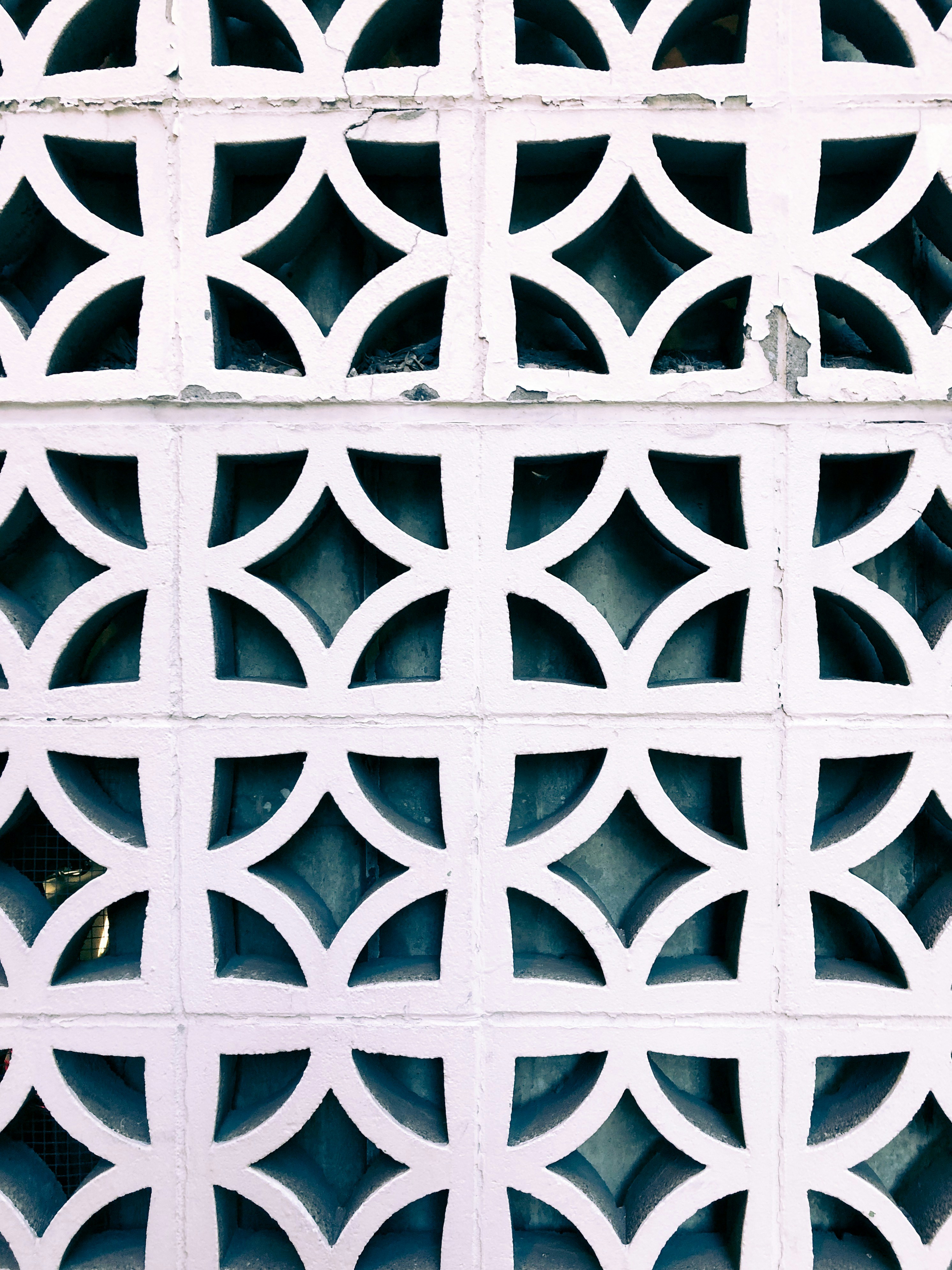 A textured wall featuring a repetitive pattern of interlocking shapes, showcasing a blend of light and shadow. The design emphasizes the interplay of geometry and color.