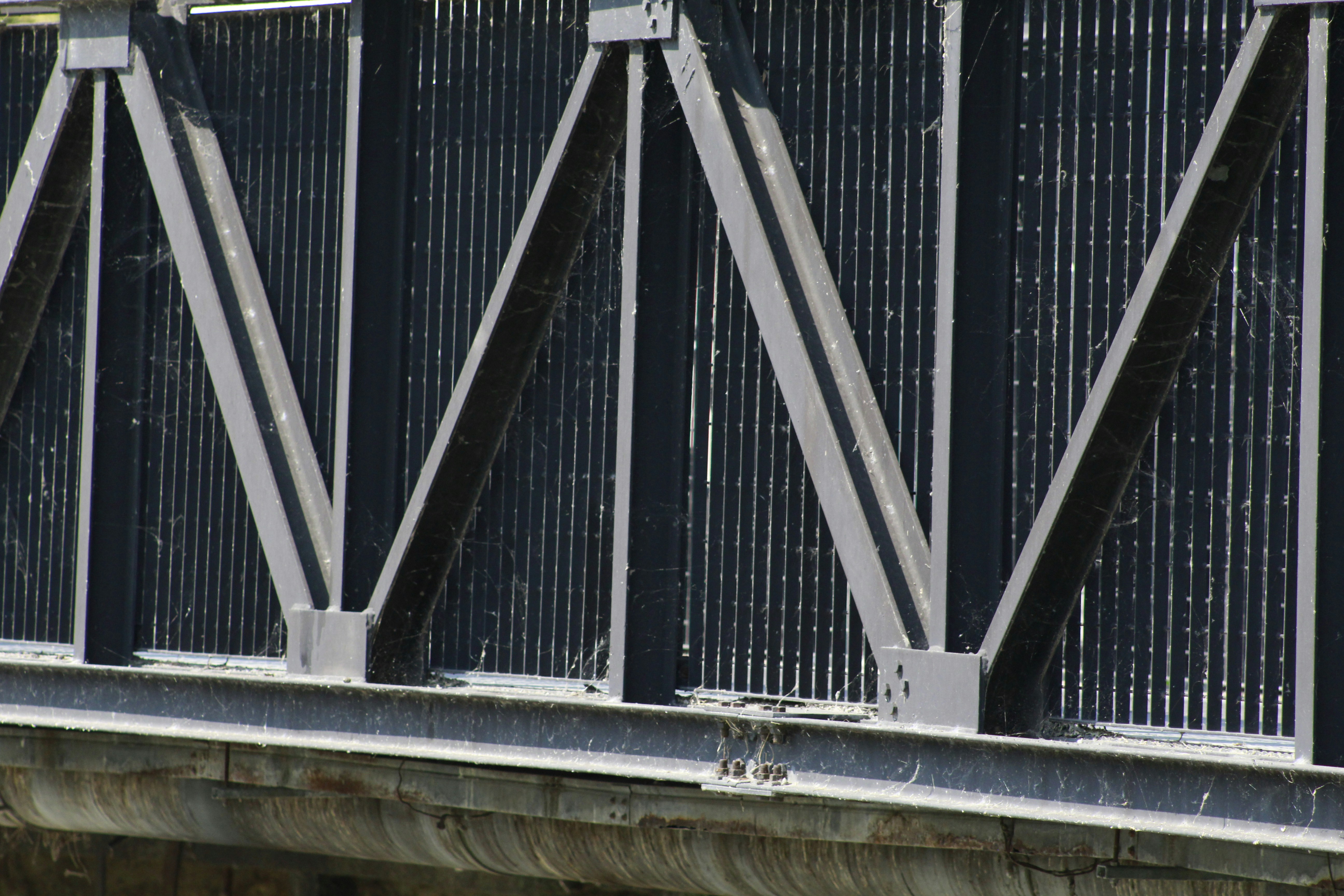 Close-up of a bridge's metal framework showcasing intricate patterns and textures. The interplay of light and shadow highlights the engineering design.