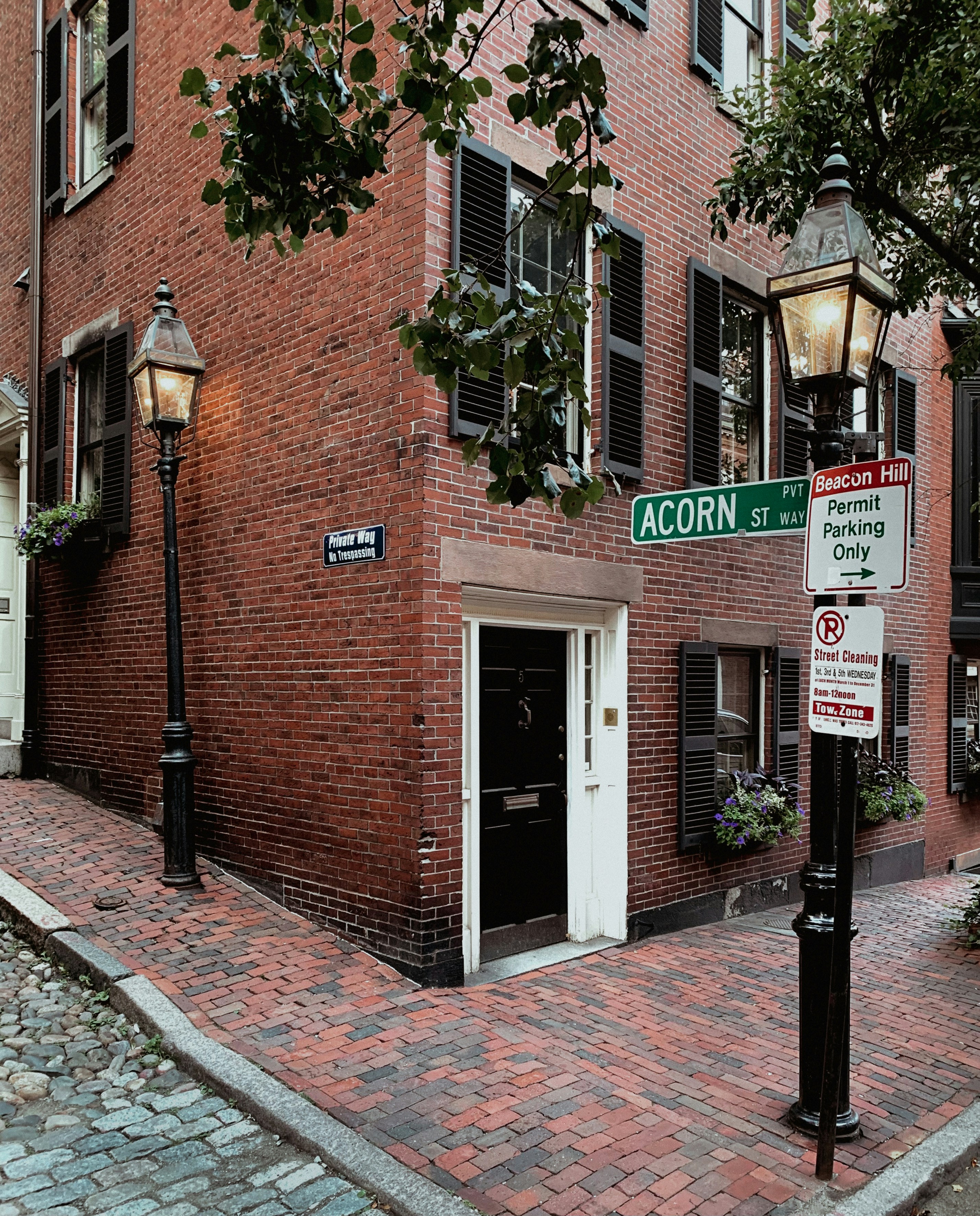 Brick Street Corner: Signs, Lanterns, and a Black Door Under Shaded Windows