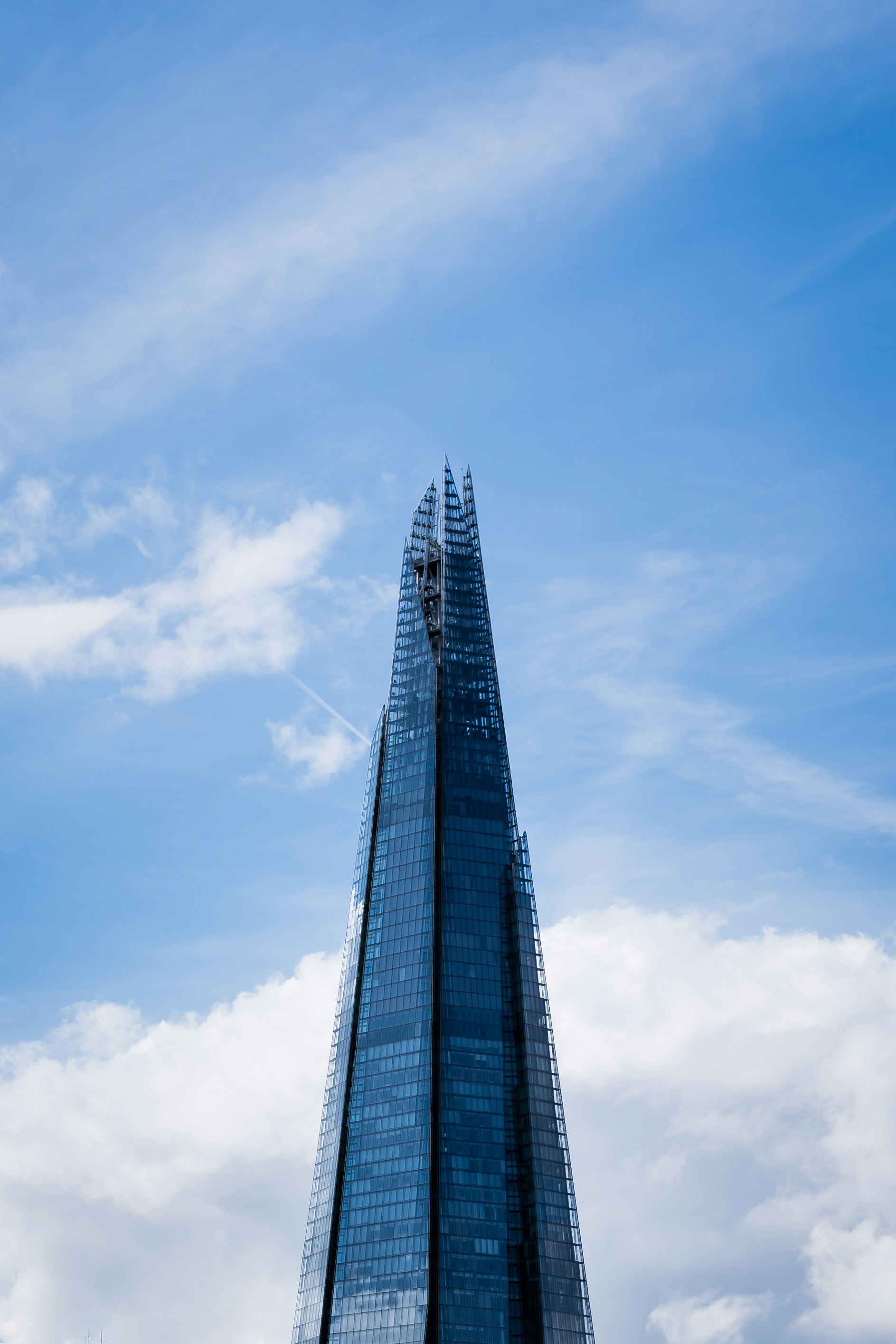 The Shard's glass facade gleams under a bright blue sky, showcasing its distinctive pointed design against a backdrop of soft clouds.