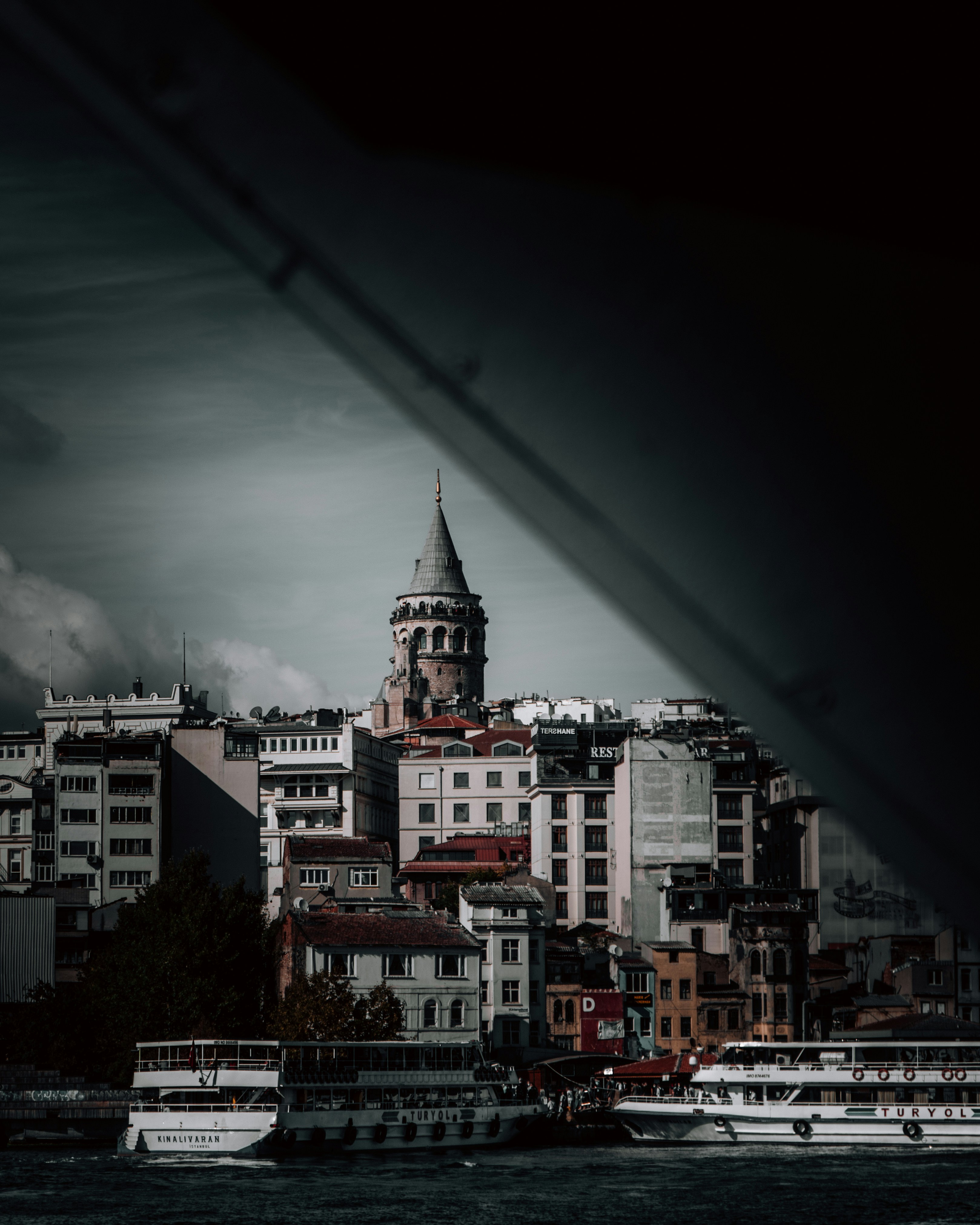 Galata Tower rises above the cityscape, framed by the silhouettes of boats and buildings, capturing a moment in Istanbul's rich history.