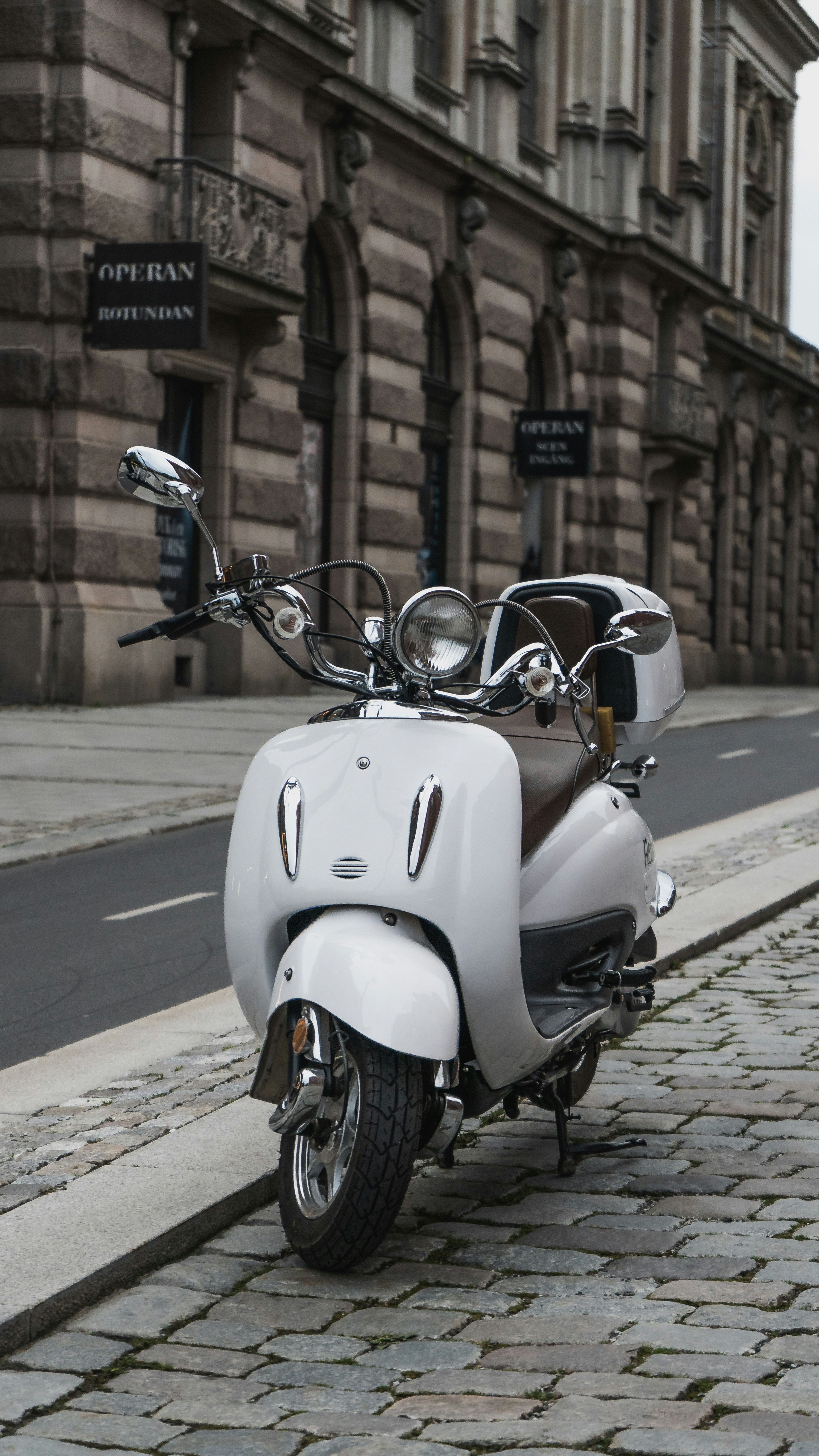 White Vespa on cobblestones under European Facades
