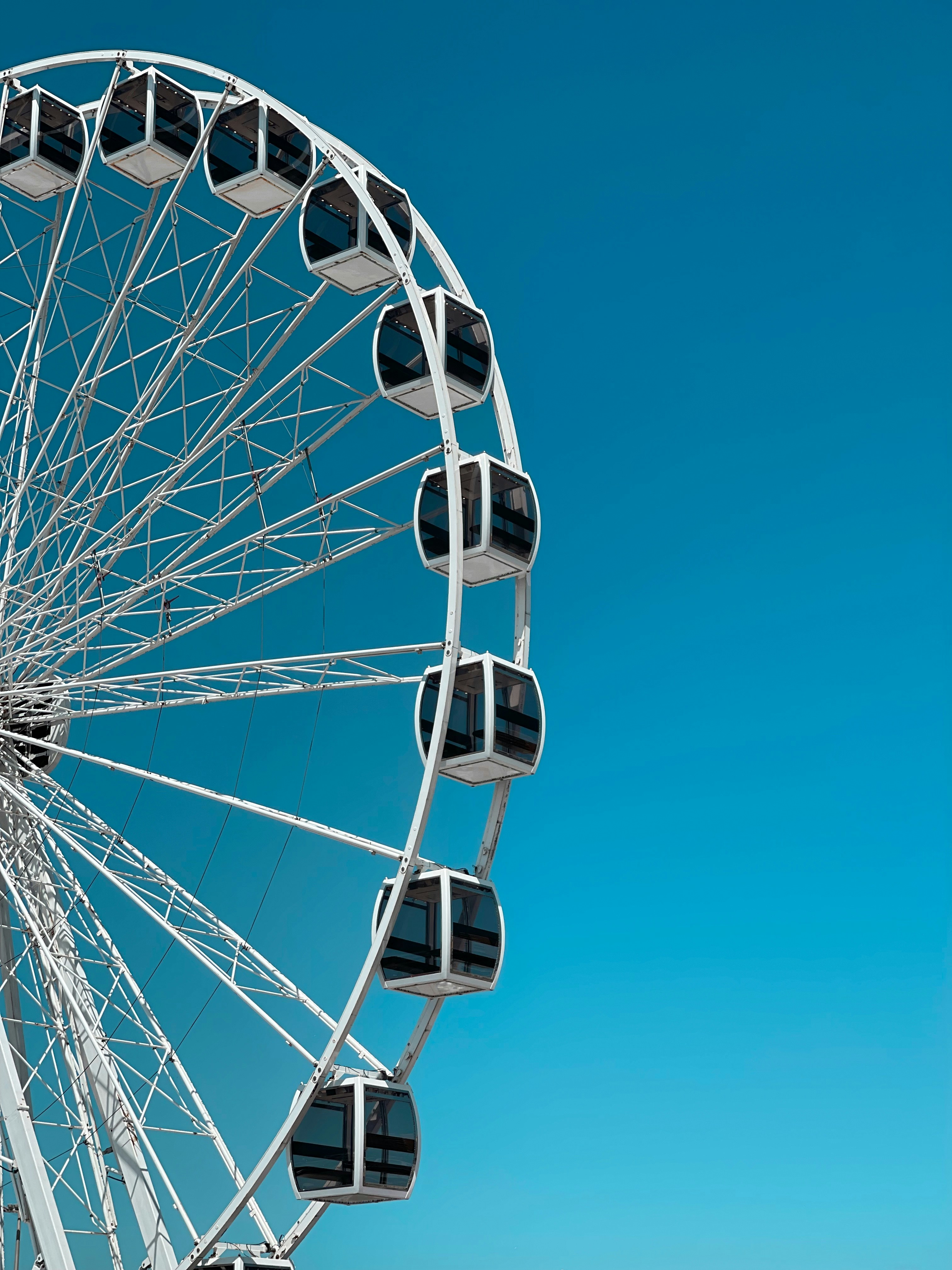 A modern Ferris wheel with transparent cabins stands against a clear blue sky, showcasing its intricate structure and design.